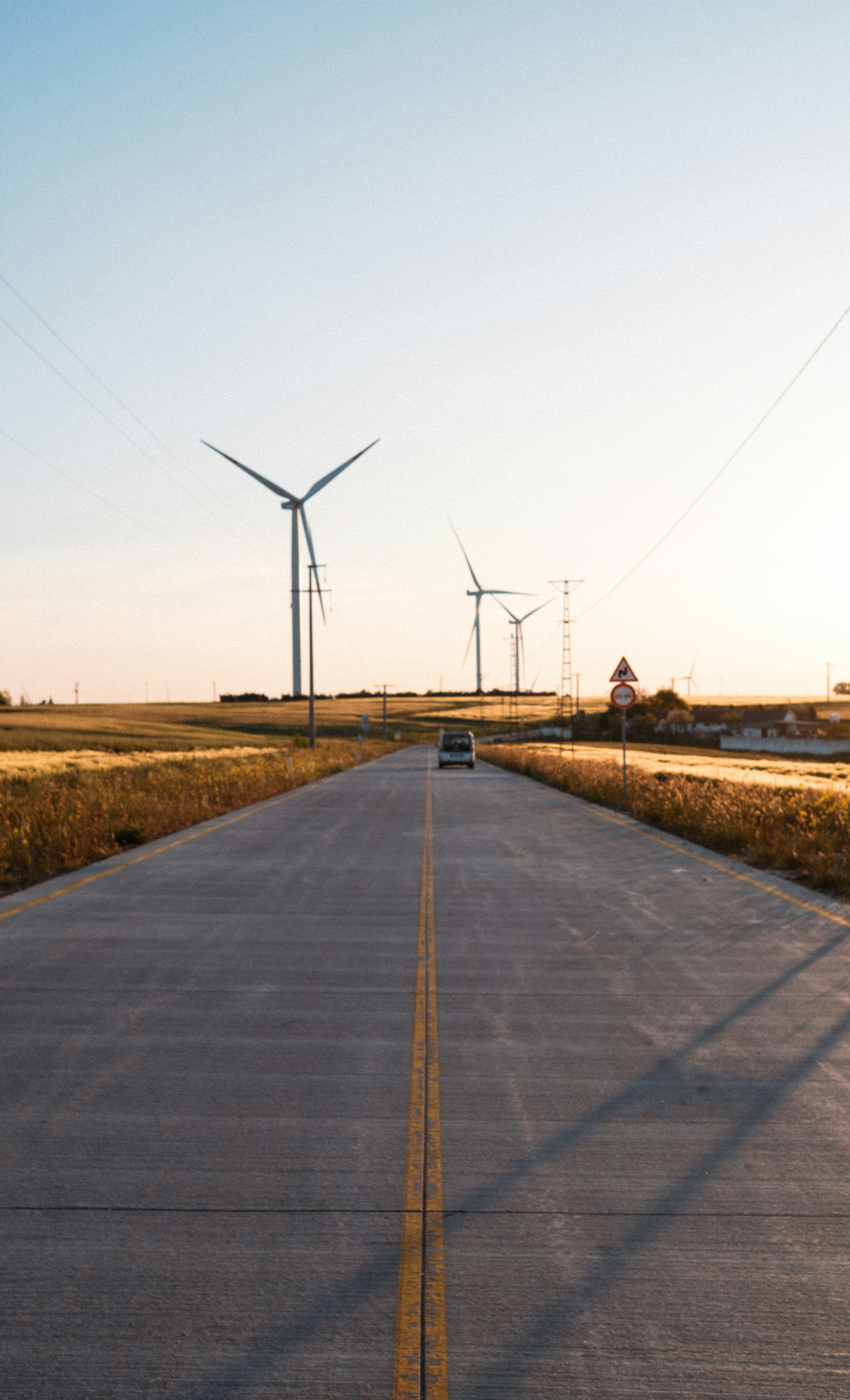 Horizon on Rails: A Quiet Road Bordered by Wind Turbines at Sunset