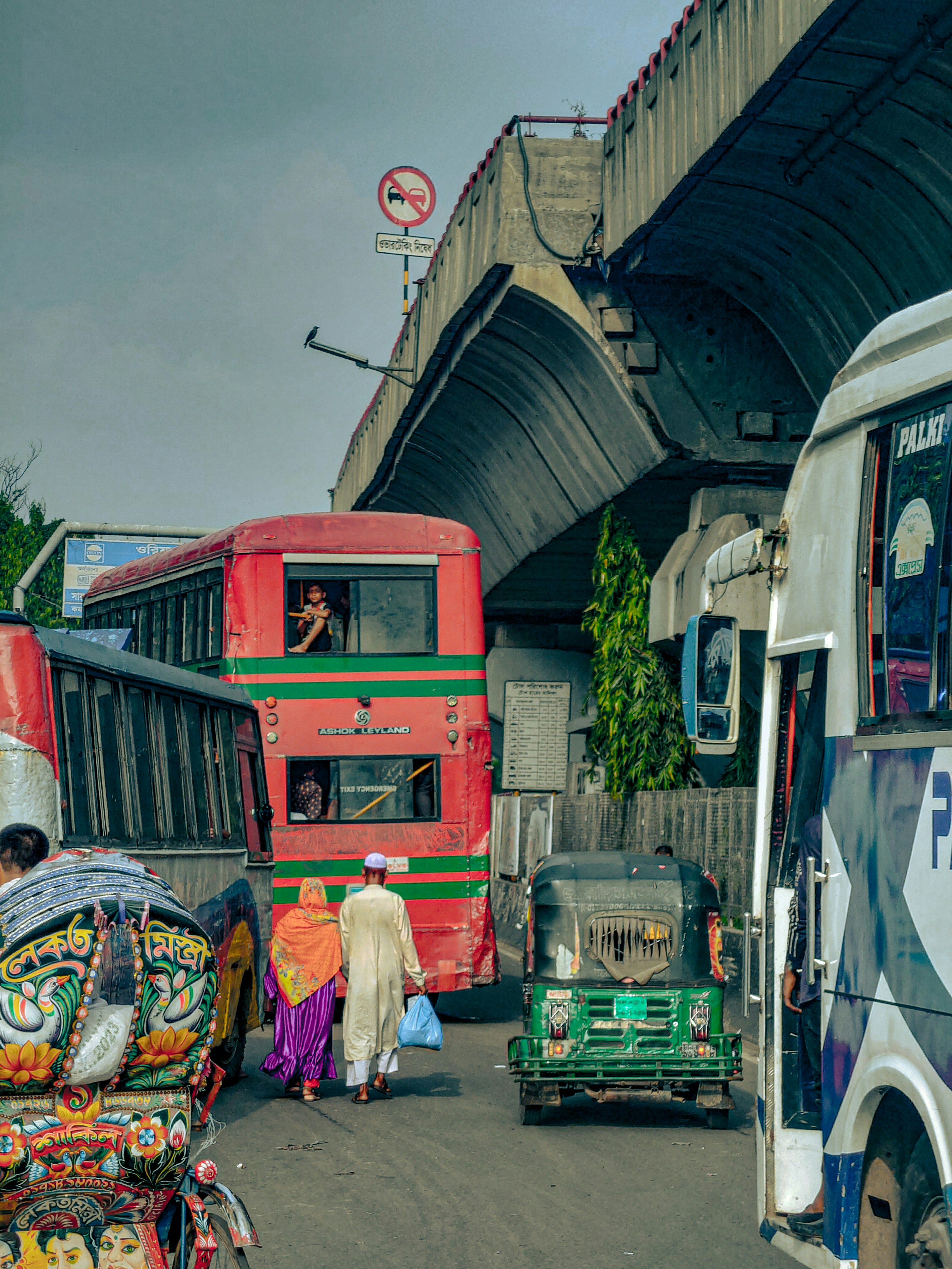 A bustling urban scene featuring colorful buses and pedestrians navigating through traffic under an overpass.