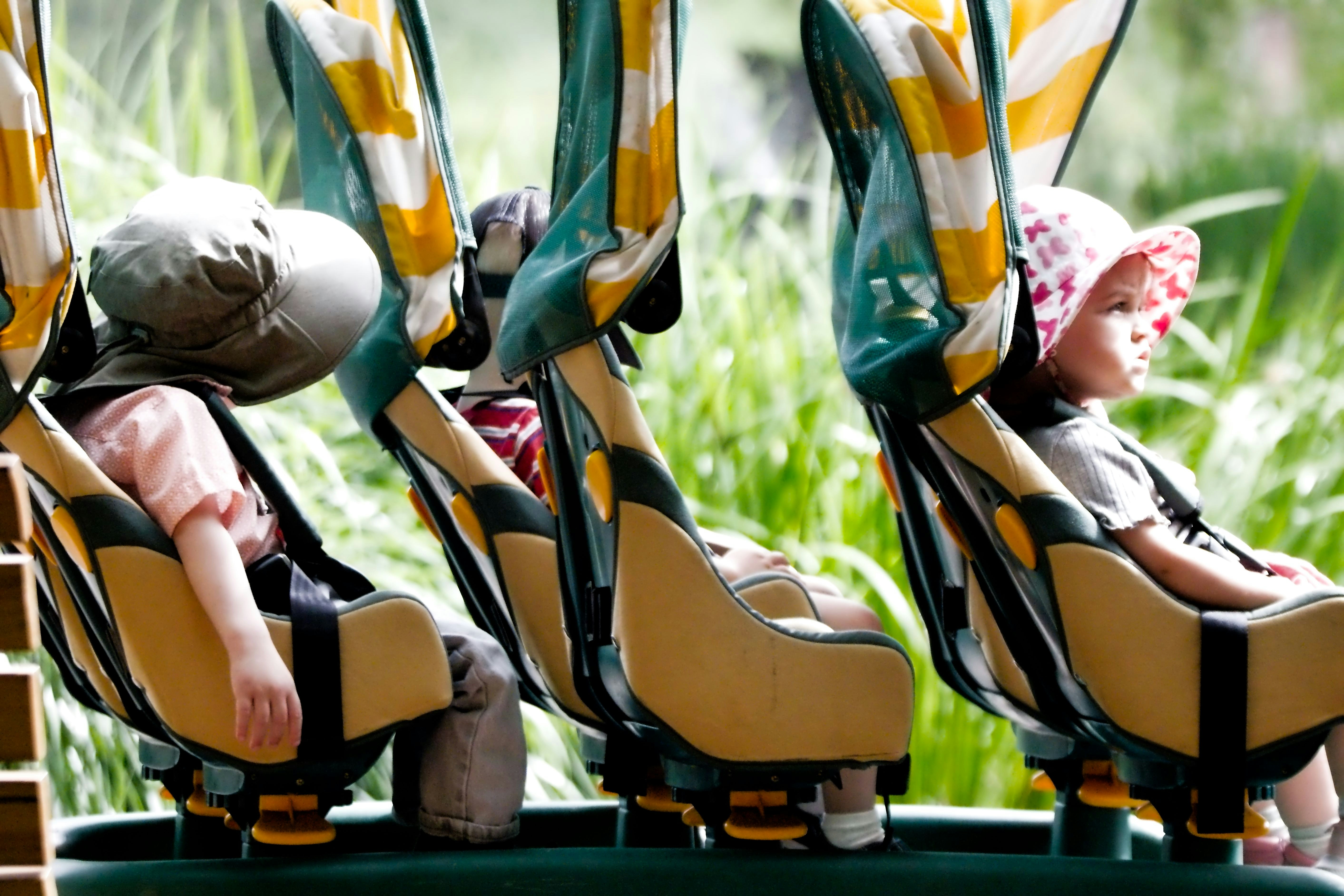 Young children with hats sit in colorful carousel seats under bright sunlight.