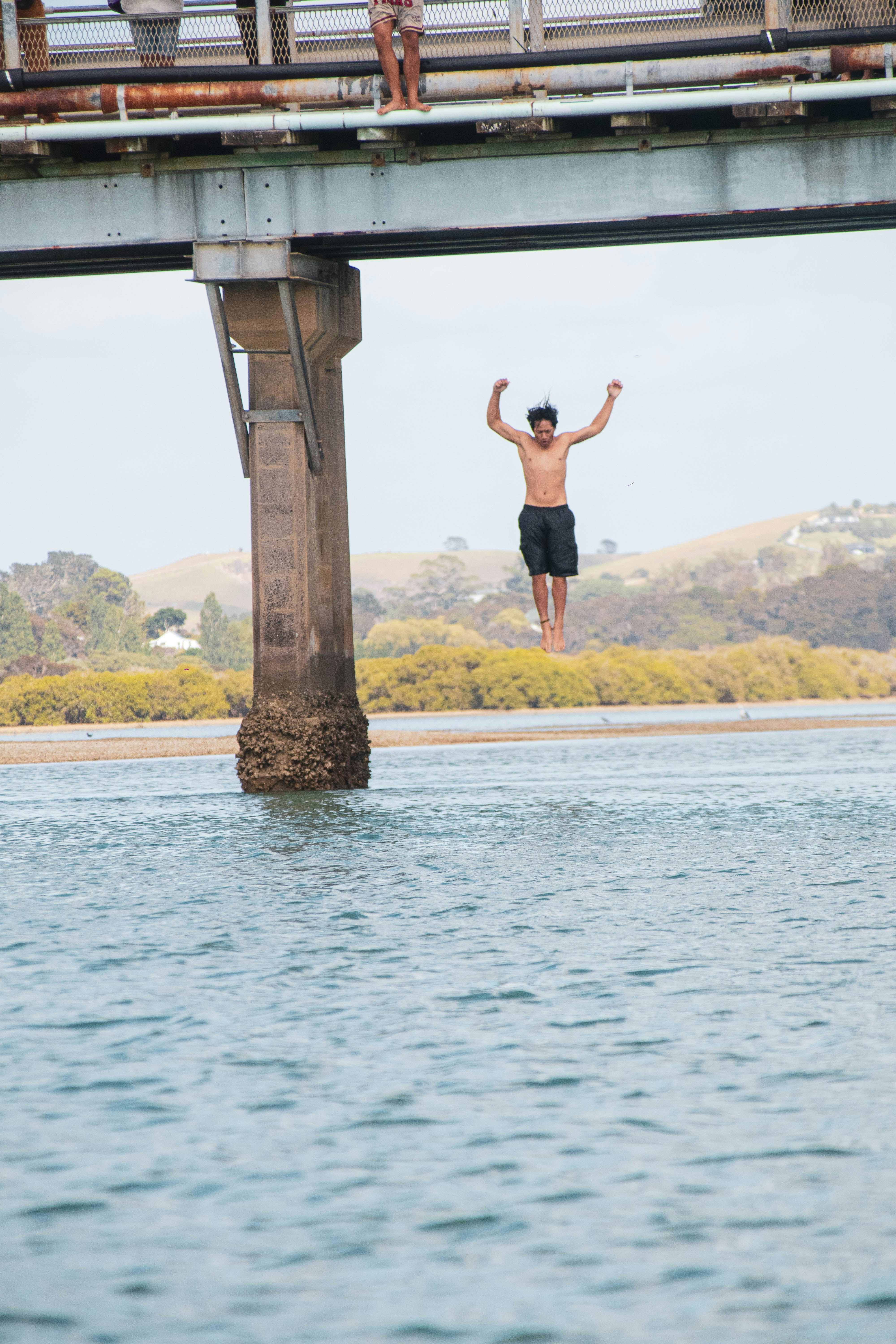 A man jumping off a bridge into a body of water photo – Free Man Image ...