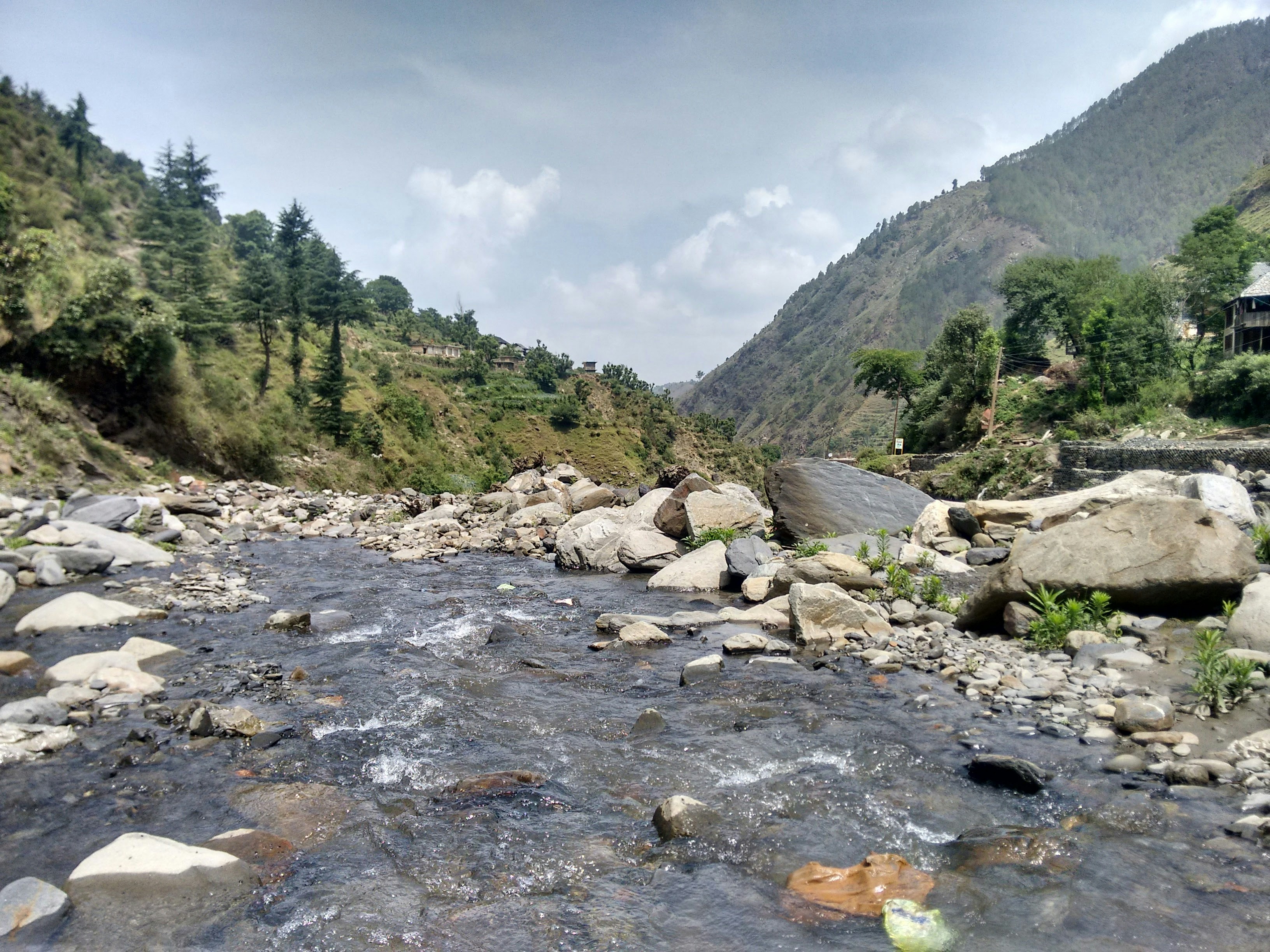 Mountain stream winding through rocky terrain flanked by lush hills and a cloudy sky.