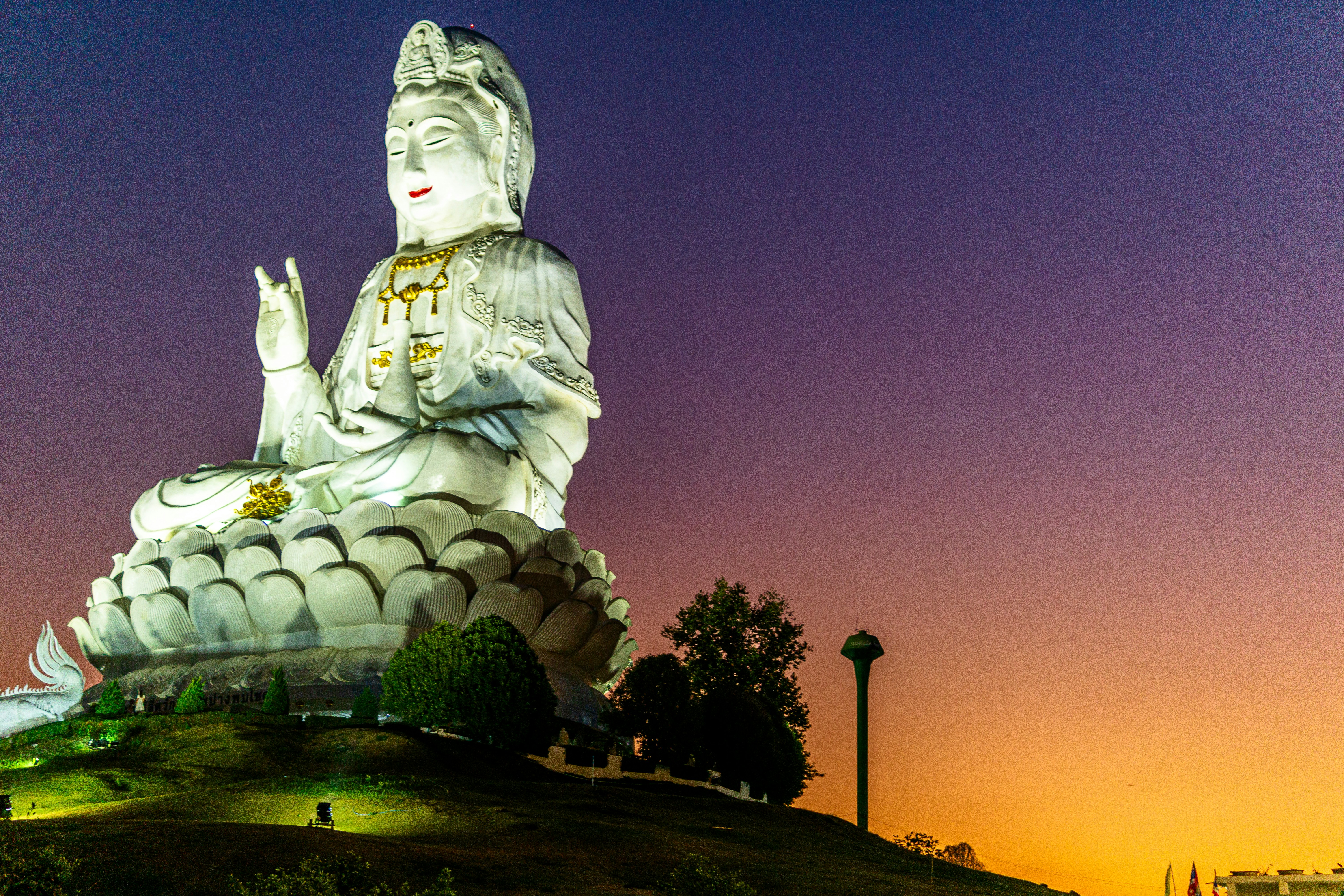 Large white Buddha statue on a hill against a vibrant sunset sky.
