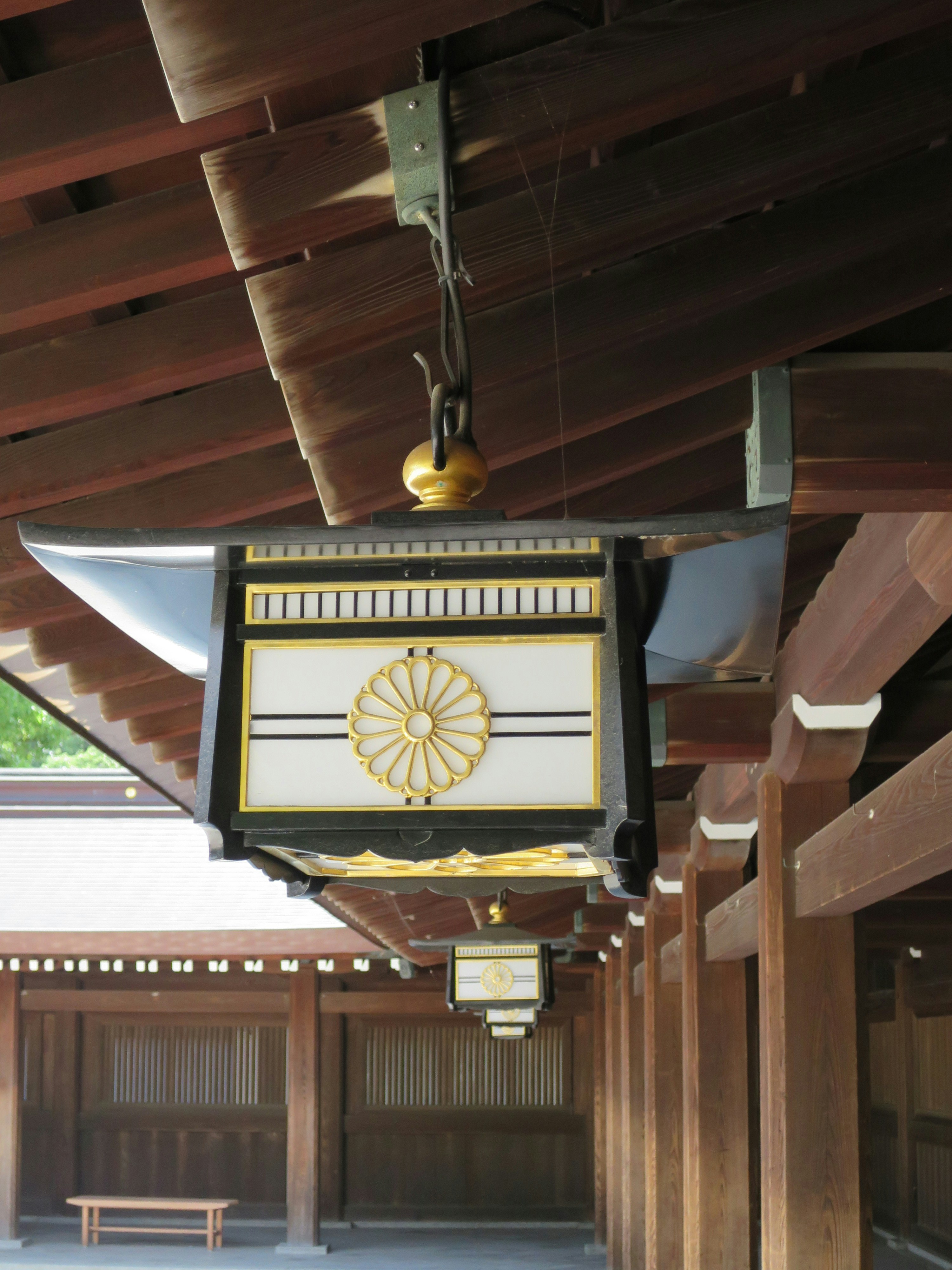 A traditional Japanese lantern with a chrysanthemum crest hangs from wooden beams, guiding the view along a shrine corridor. The scene emphasizes architectural detail and the ceremonial atmosphere.