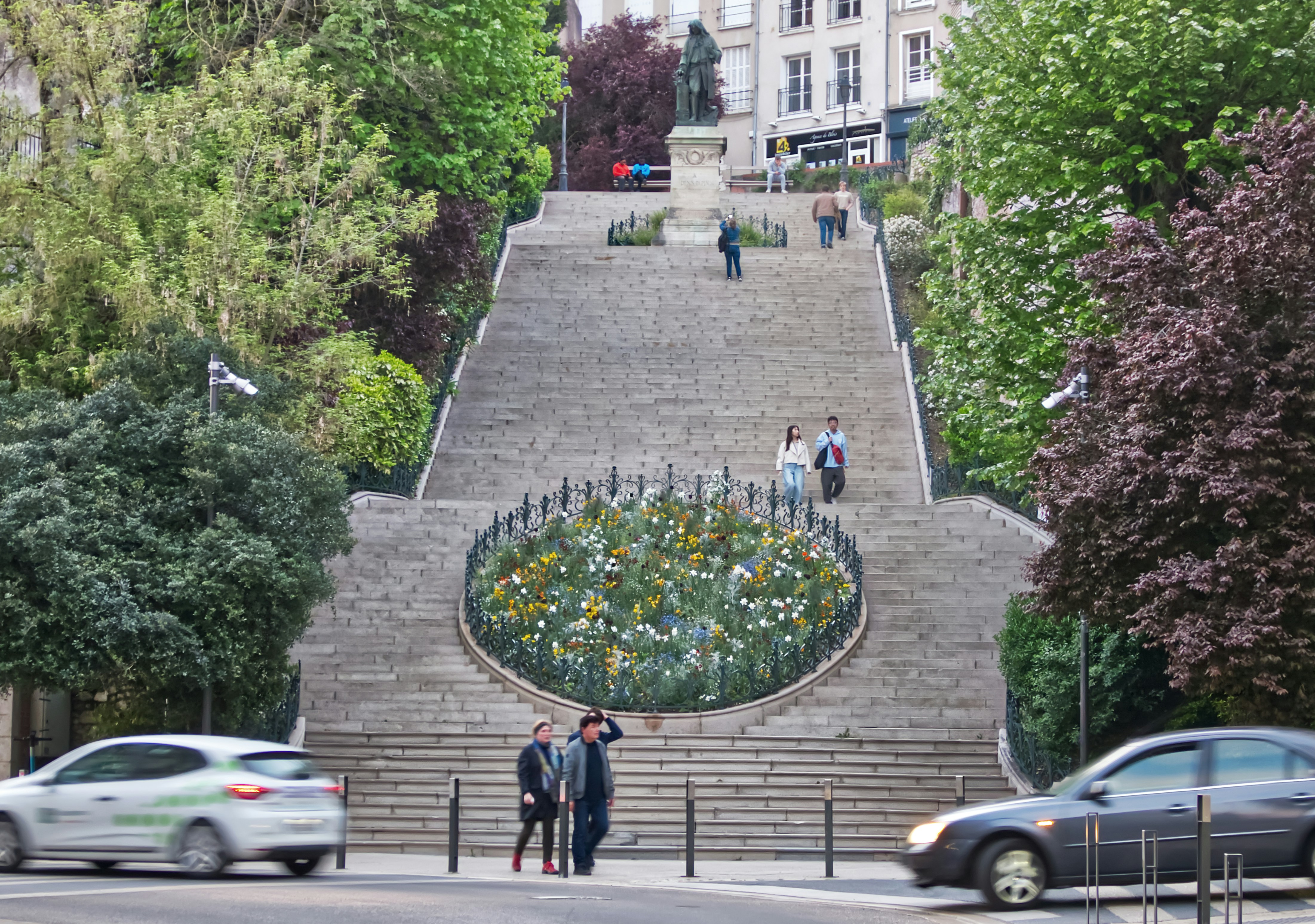 Grand staircase adorned with circular floral arrangement, flanked by lush greenery and urban architecture.