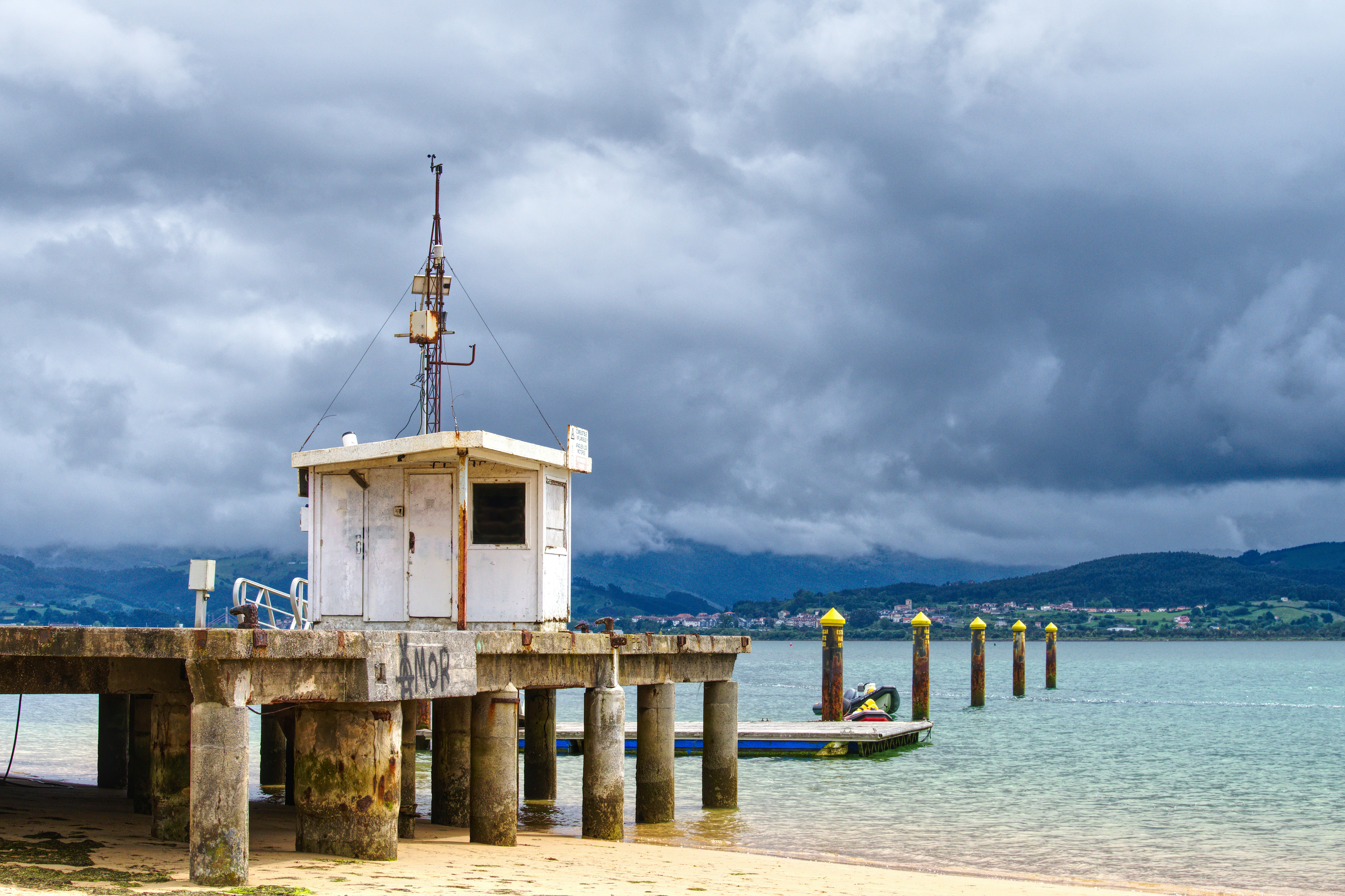 Small dockside shack with dramatic clouds over a calm sea.