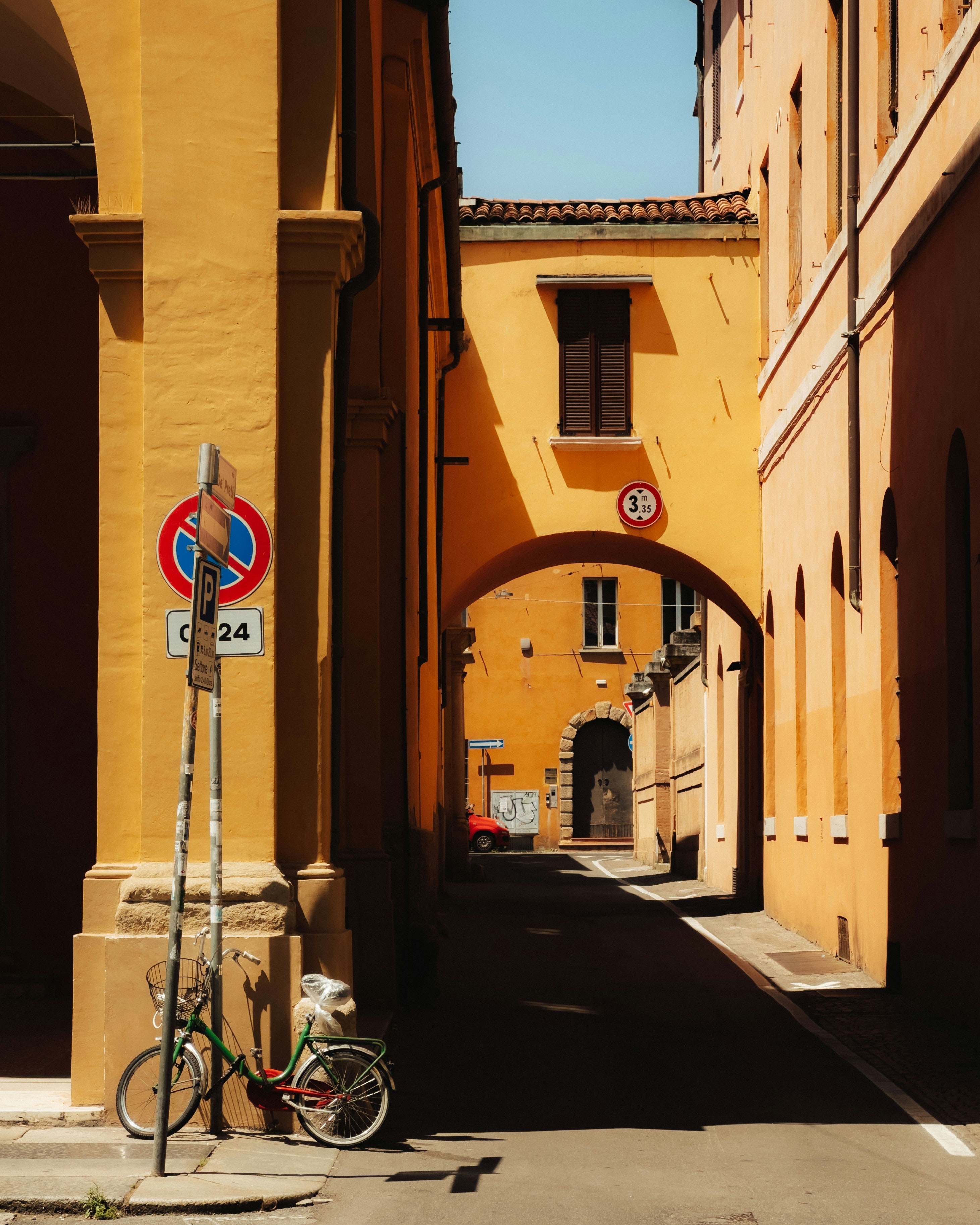 Narrow alleyway framed by vibrant yellow buildings, showcasing an archway and a parked bicycle. The scene invites exploration and curiosity.