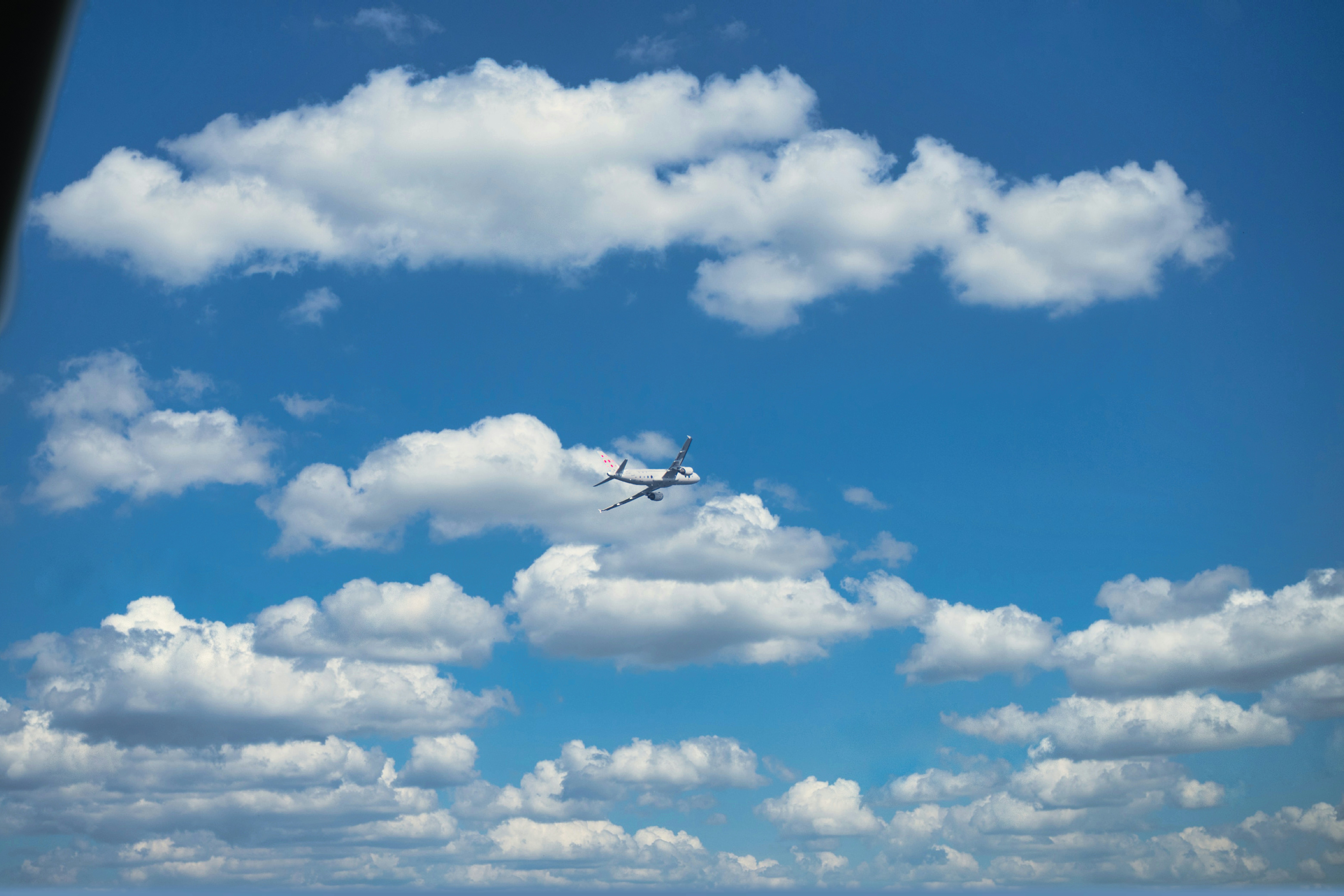 Cotton-Cloud Corridor: A Lone Plane Crossing a Bright Blue Expanse