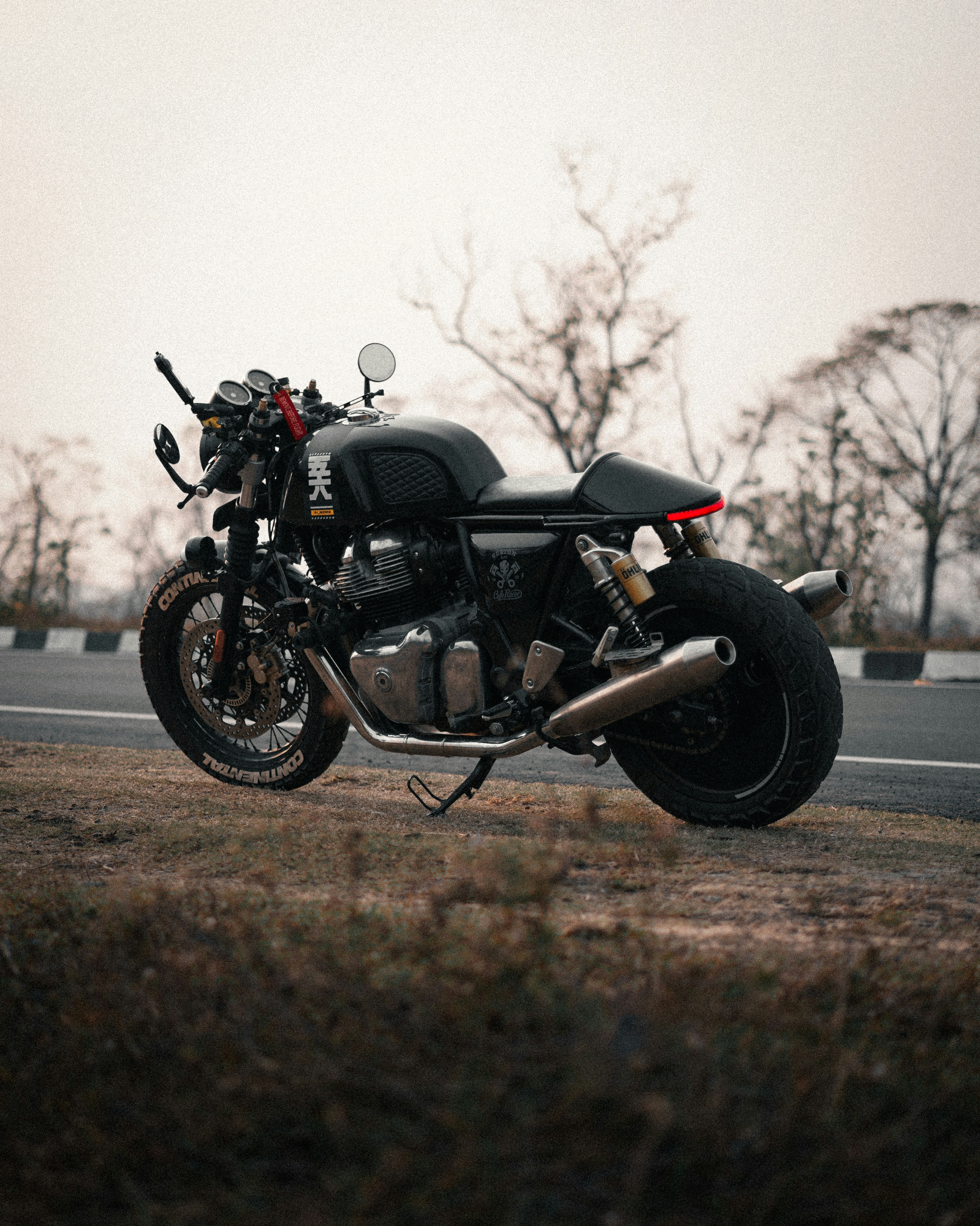 Black motorcycle parked by the roadside, showcasing its sleek design against a backdrop of bare trees and a hazy atmosphere.