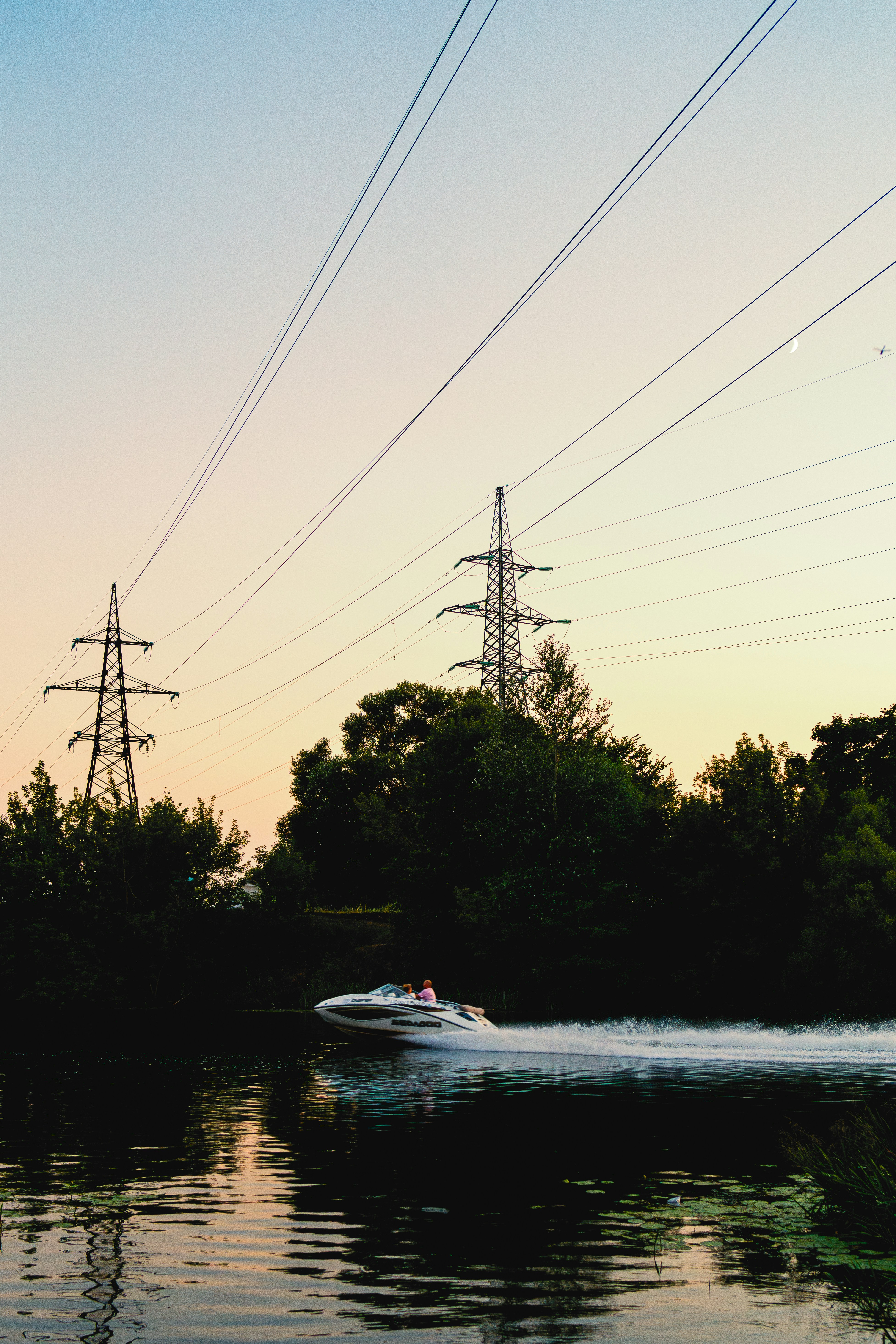 Twilight Wake: A White Speedboat Traverses a Quiet River Under Crossing Power Lines