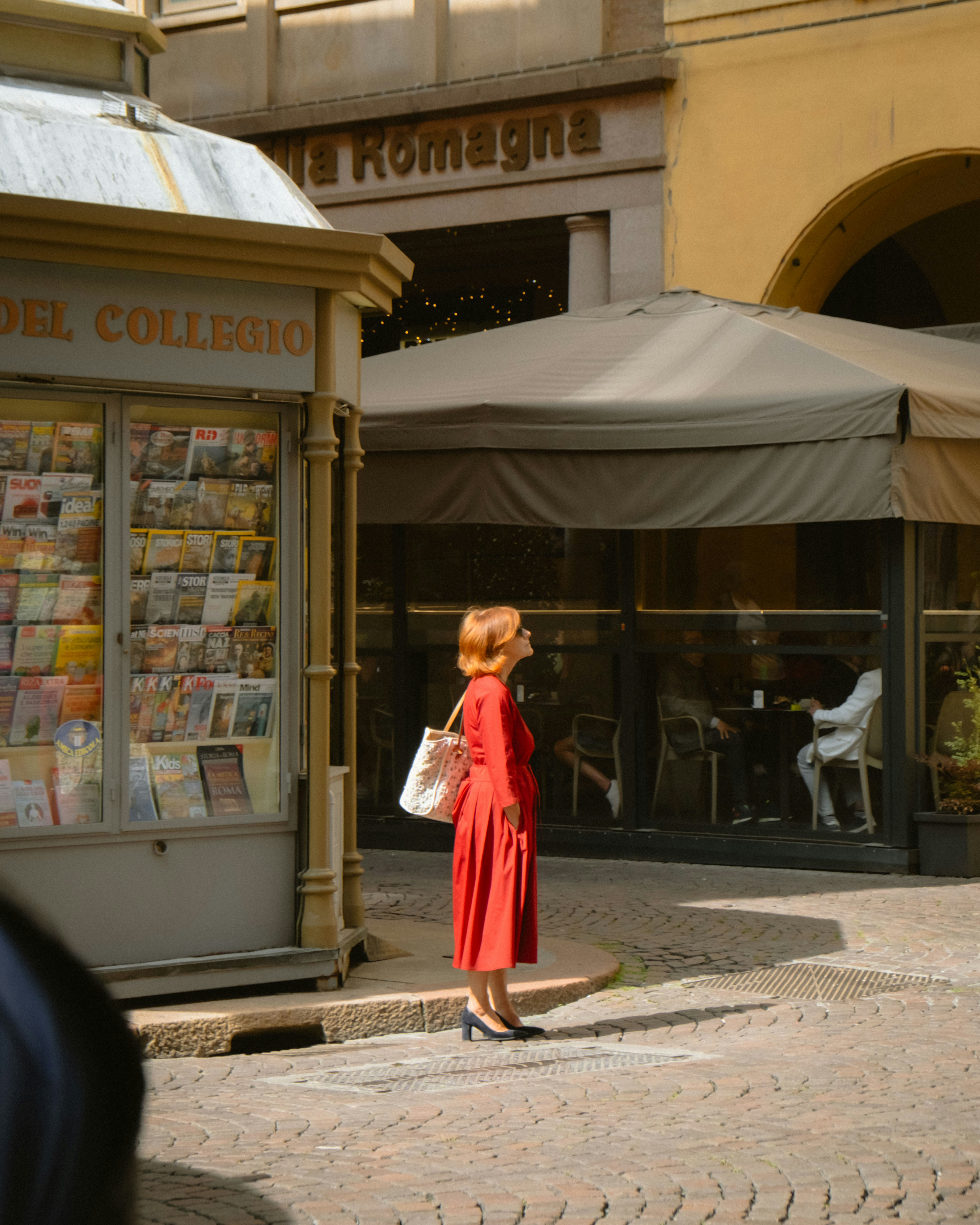 Crimson-dressed Pause on a Sunlit Cobblestone Street by a European Café