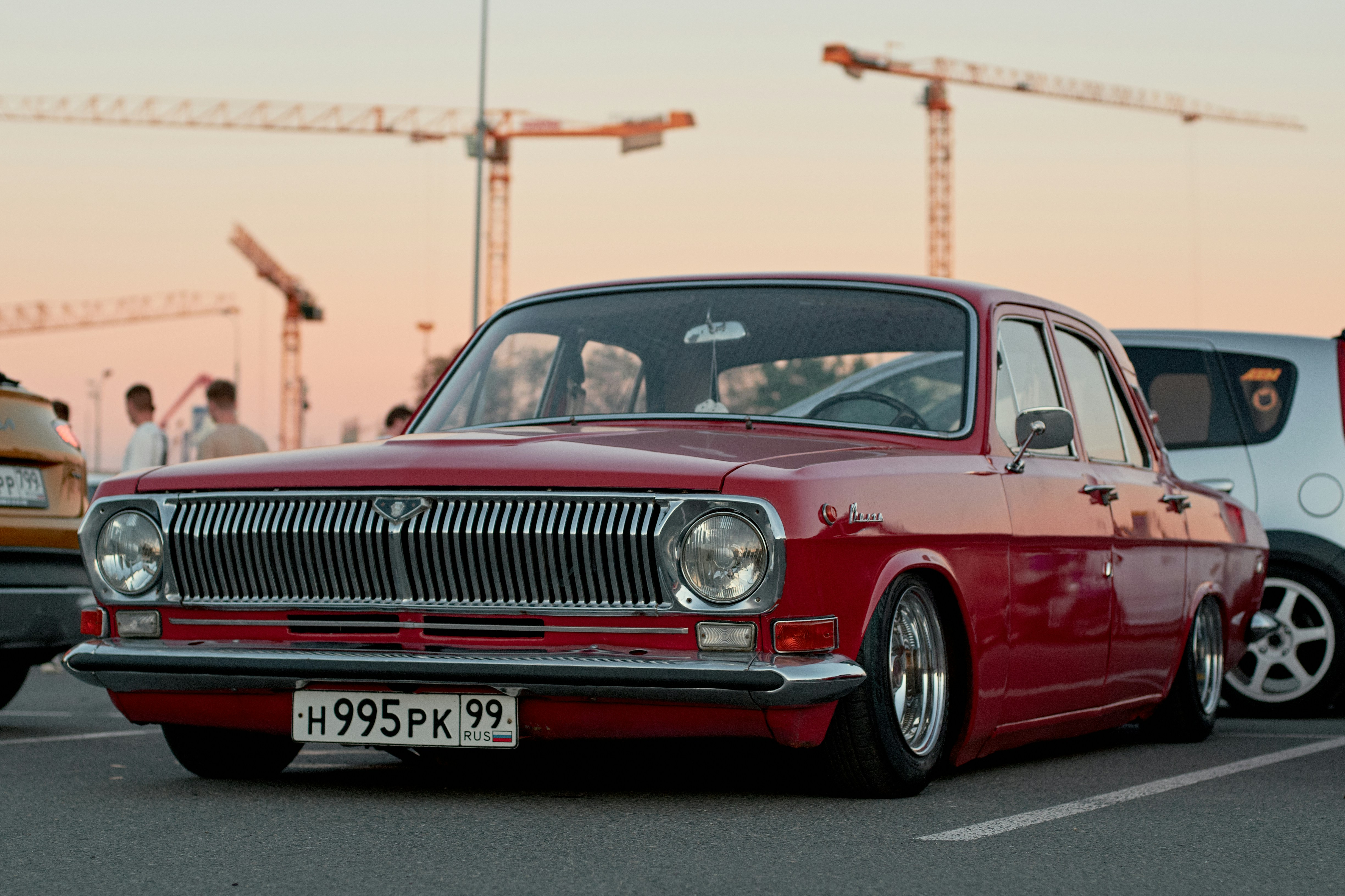 Classic red sedan parked in an urban setting, showcasing its vintage design against a backdrop of construction cranes.