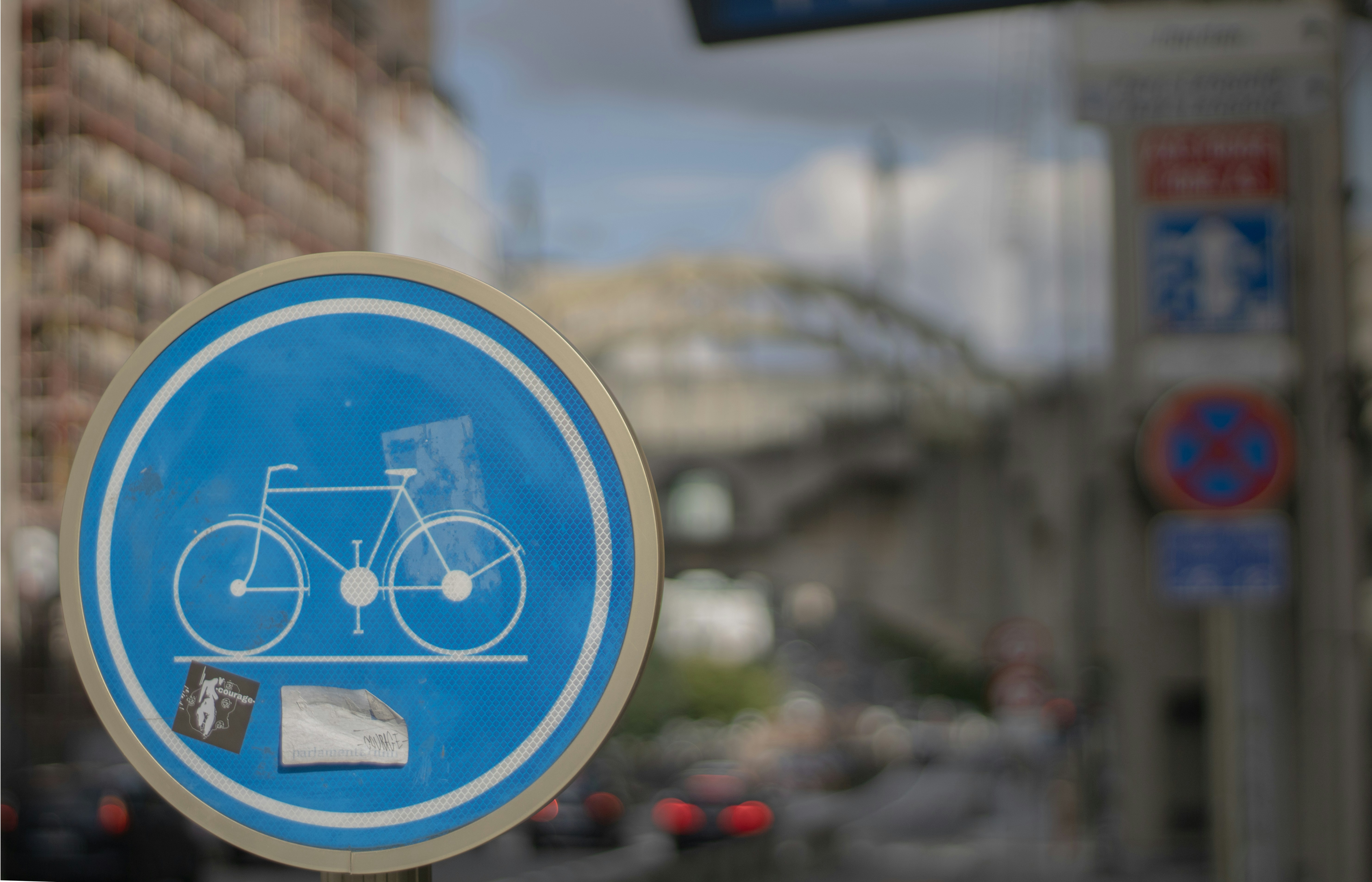Urban Carousel: Blue Bicycle Sign in Sharp Focus Amid Soft City Blur