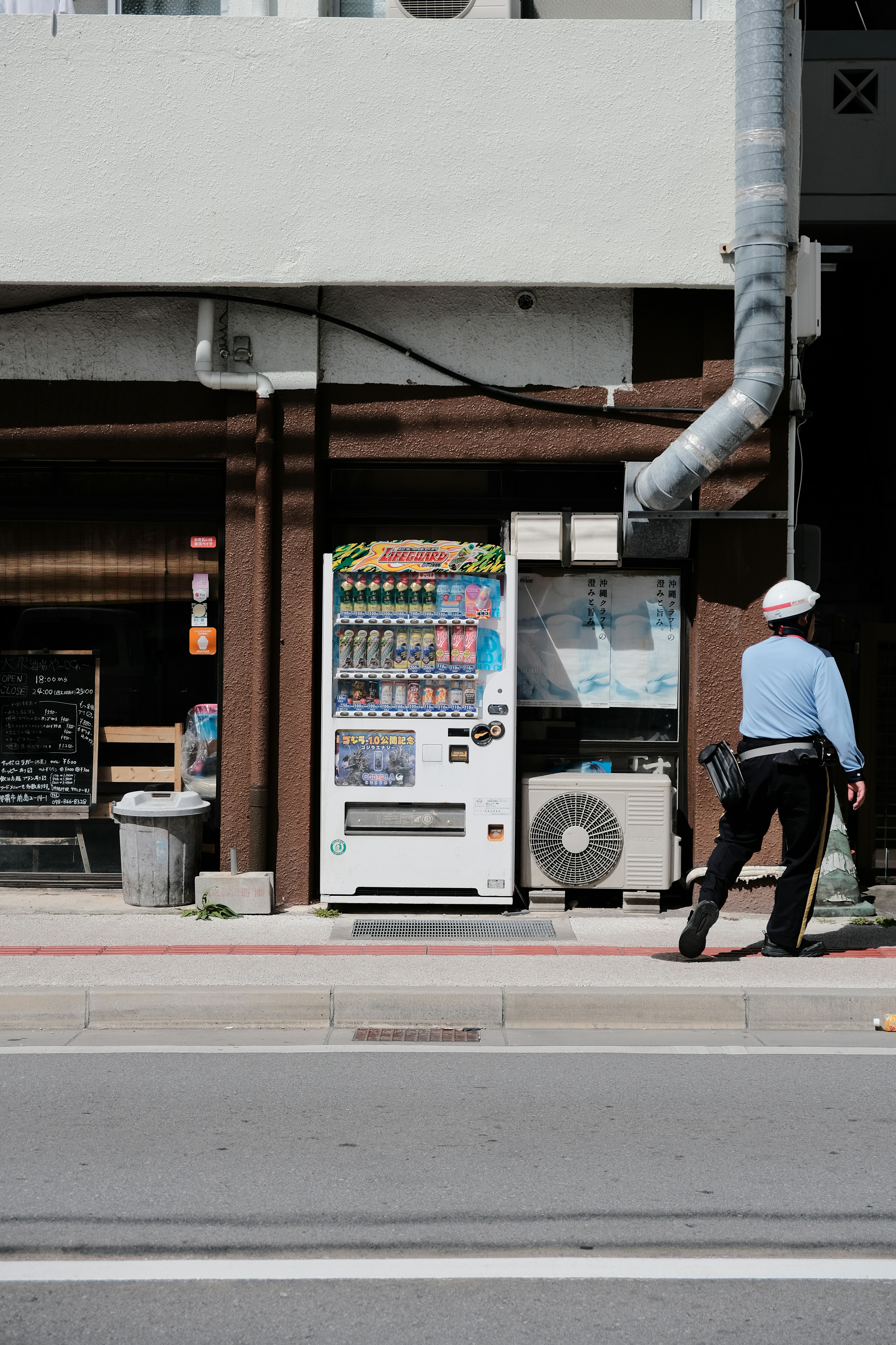 A man walking down a street next to a vending machine photo – Free Naha ...