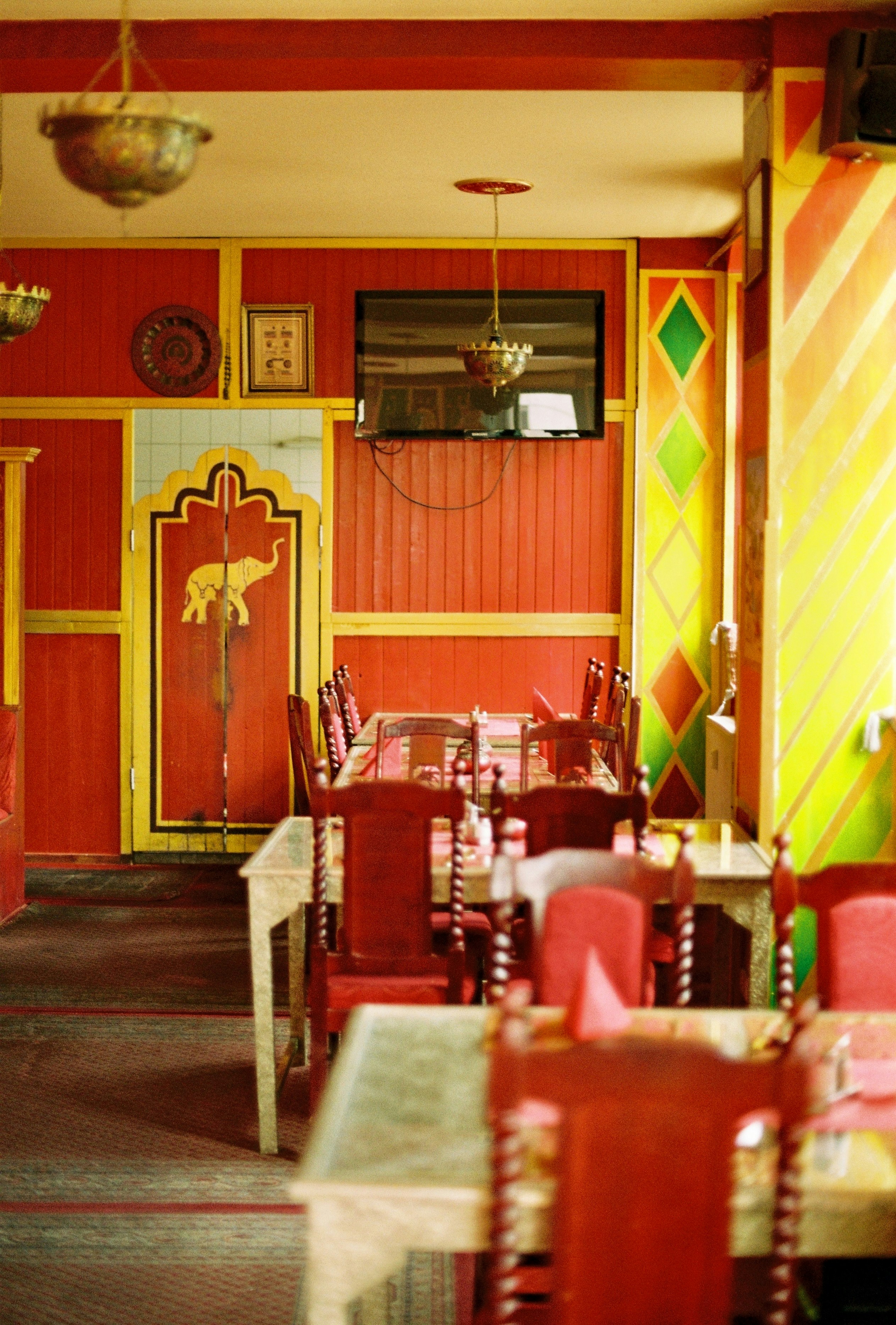 Interior photograph of a colorful dining room featuring a decorative elephant doorway and geometric walls in red, yellow, and green tones.