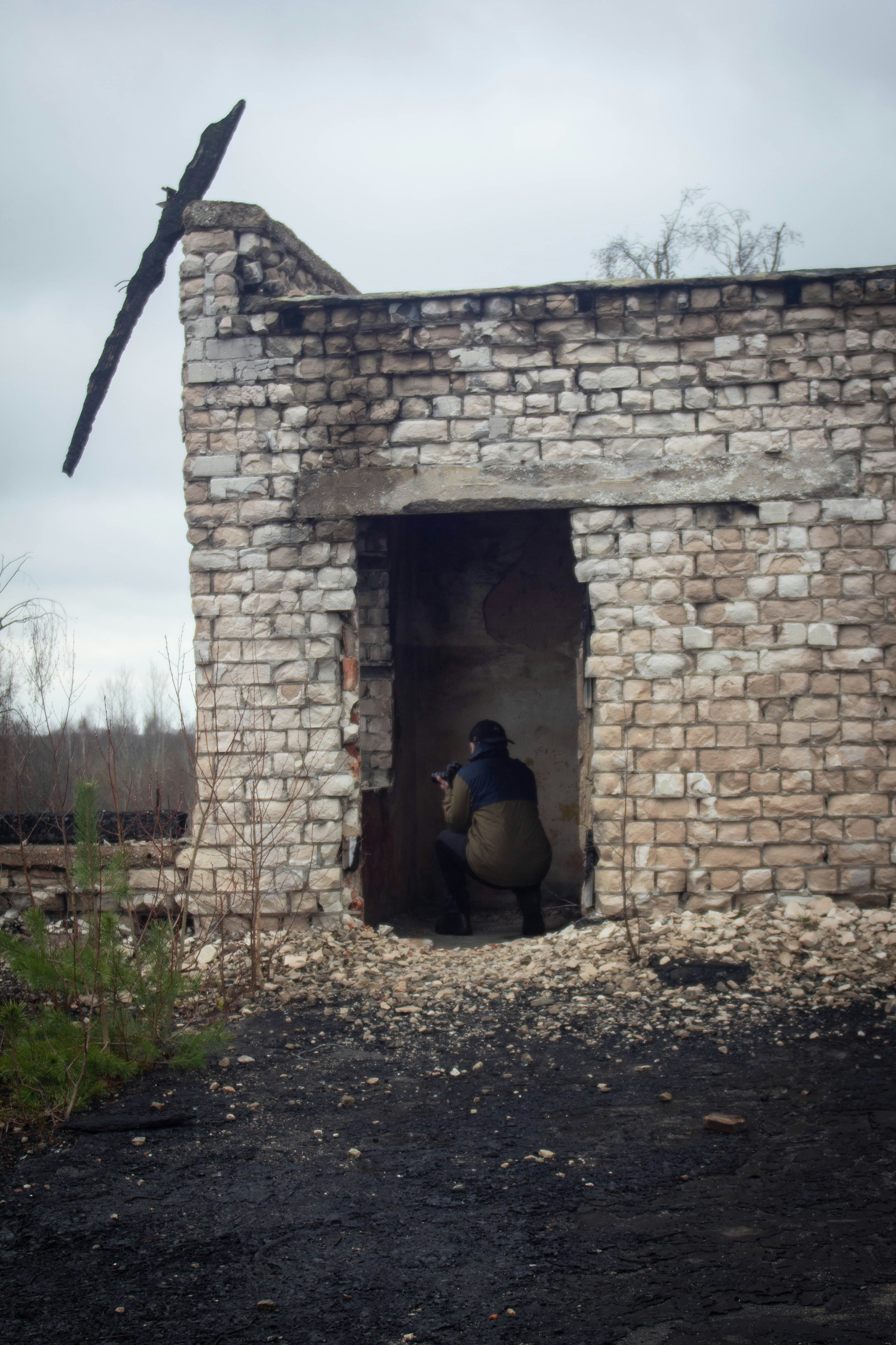 Lone photographer crouches inside a weathered doorway of a ruined stone building