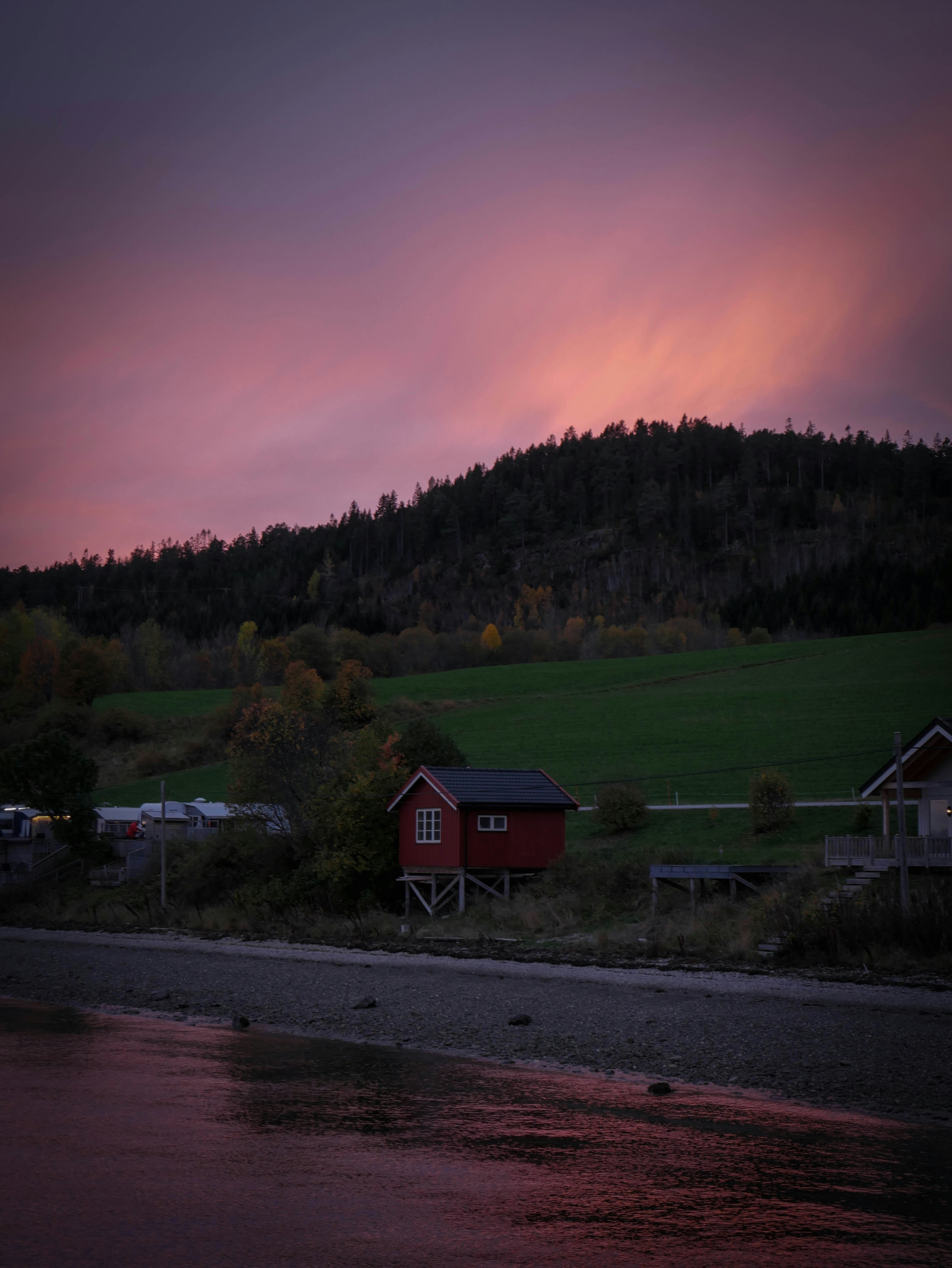 Crimson Cabin at Dusk: Riverbend Under a Pink-Cloud Sunset