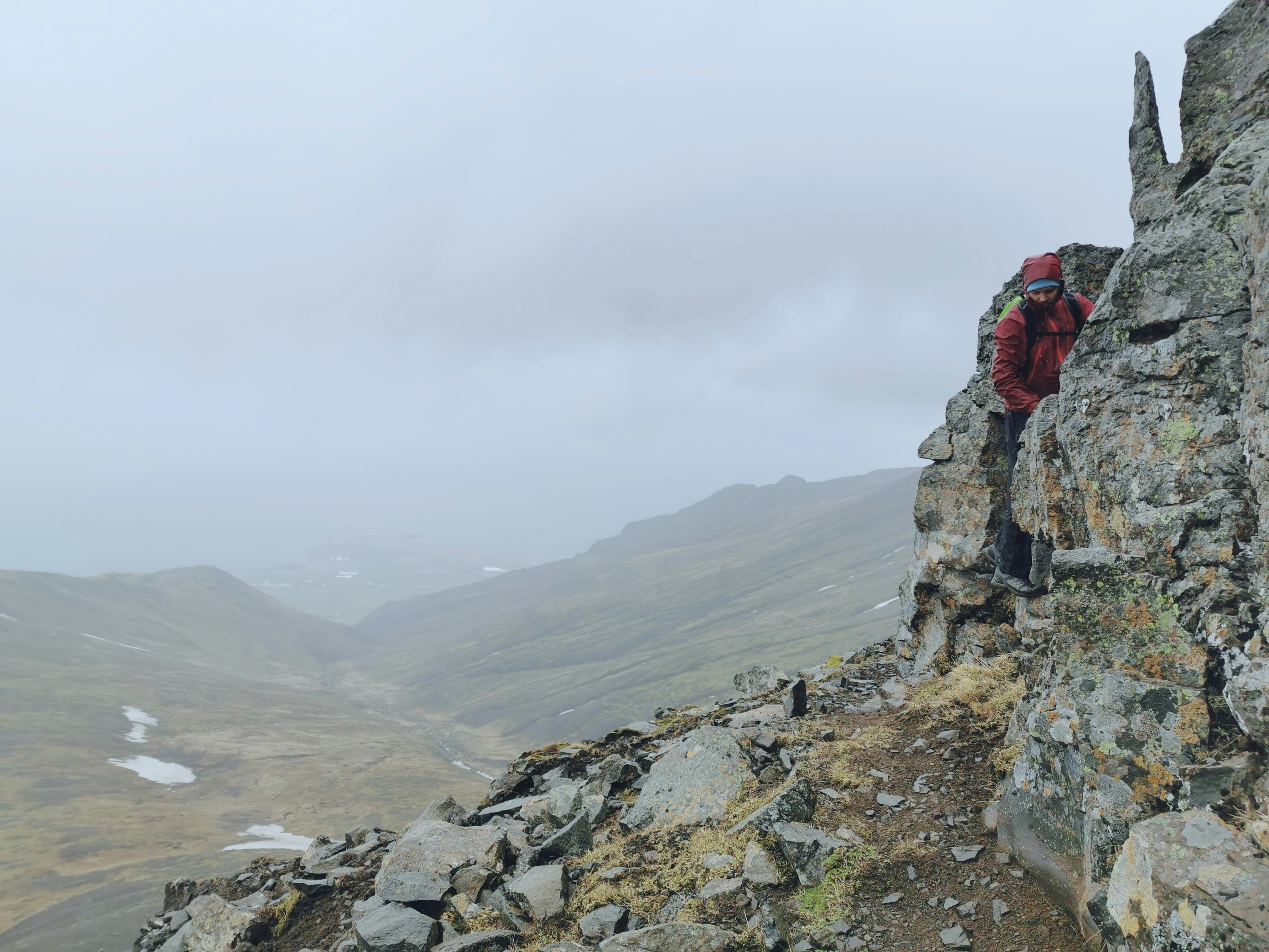 Climber navigating a rocky ledge on a foggy mountain trail, showcasing the rugged terrain and challenging conditions.