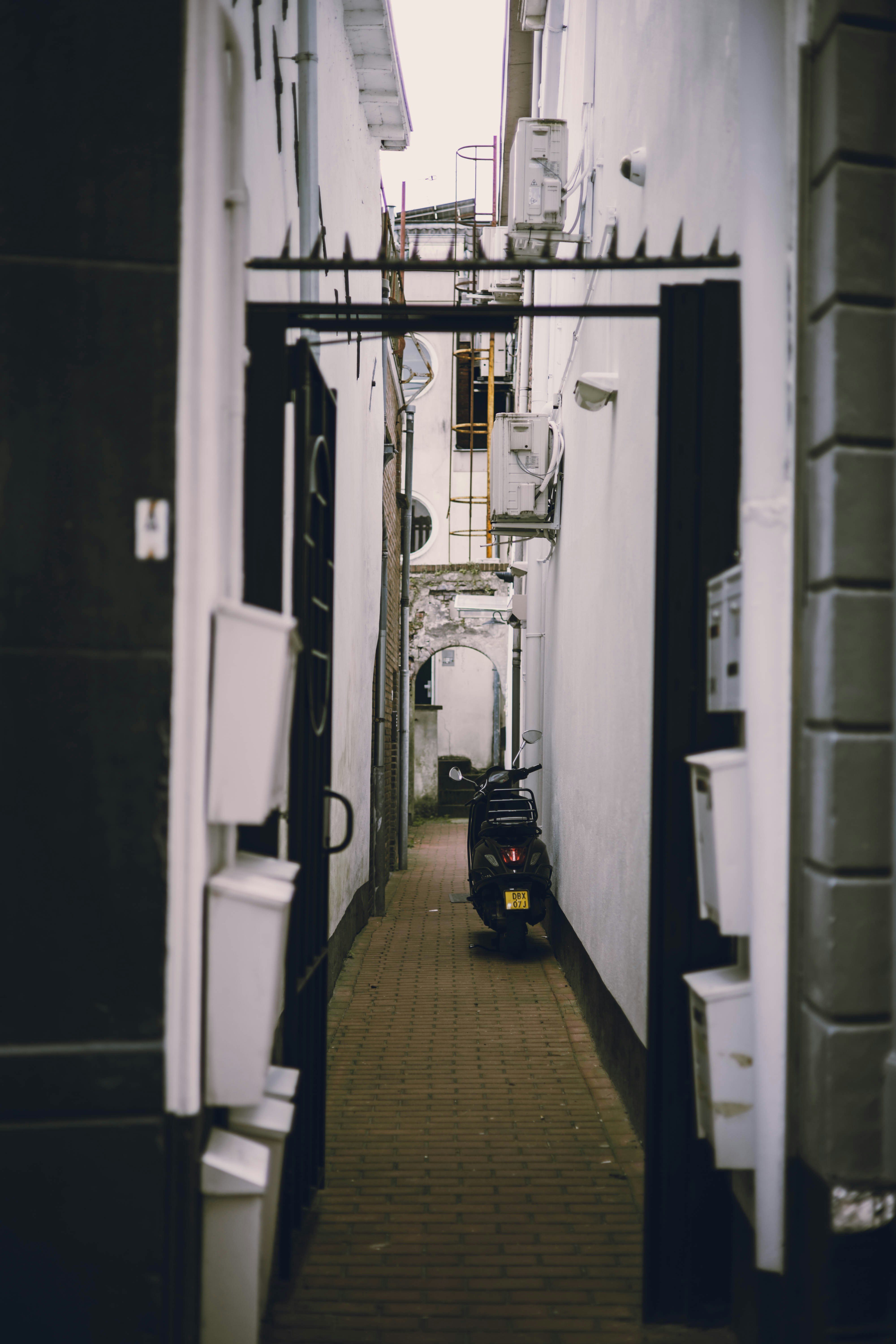 Vanishing Lines: Scooter at the End of a Narrow White Alley