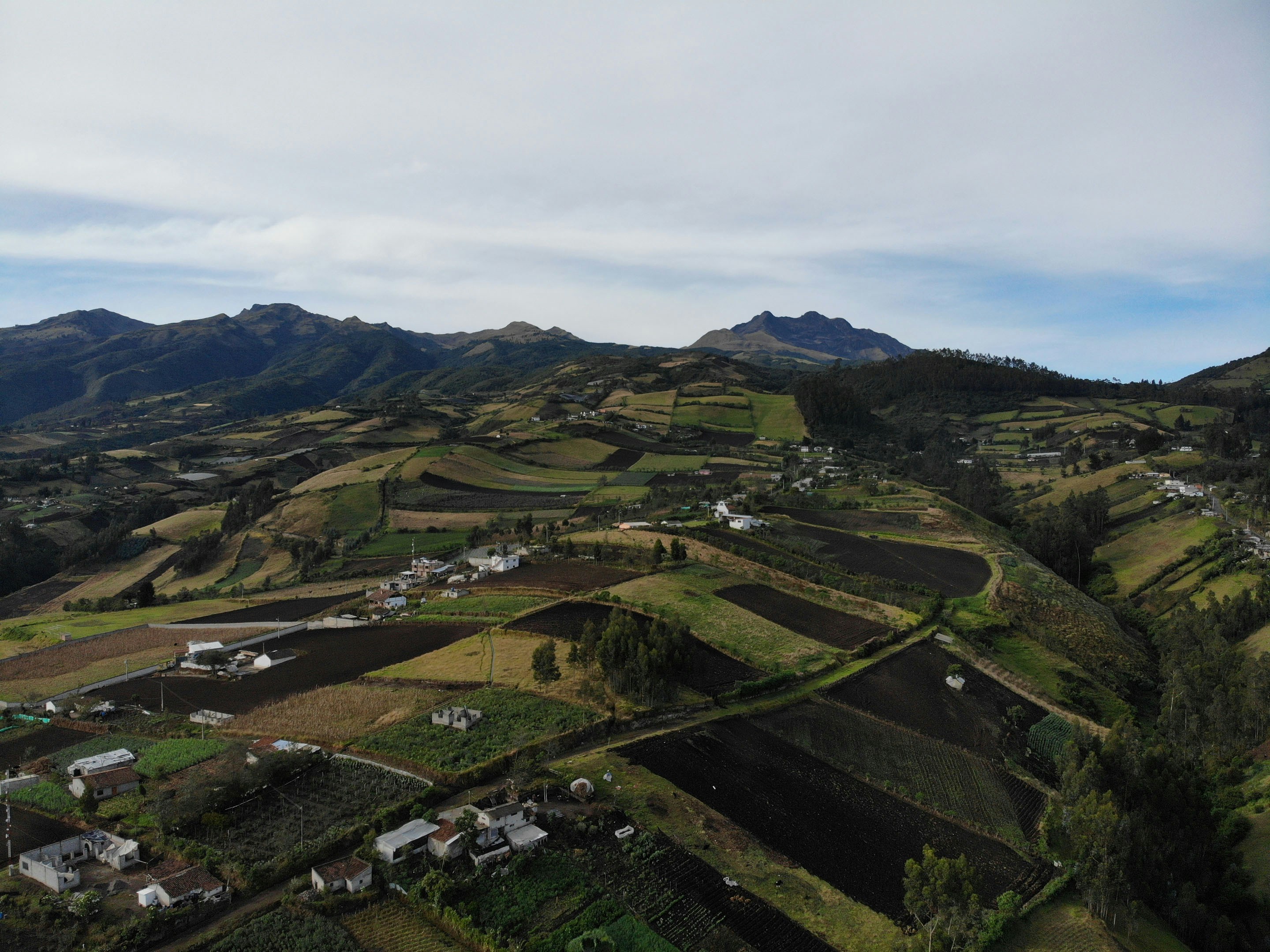 Drone view of Ecuadorian Andes landscape with different fields and tones of greens on a cloudy day