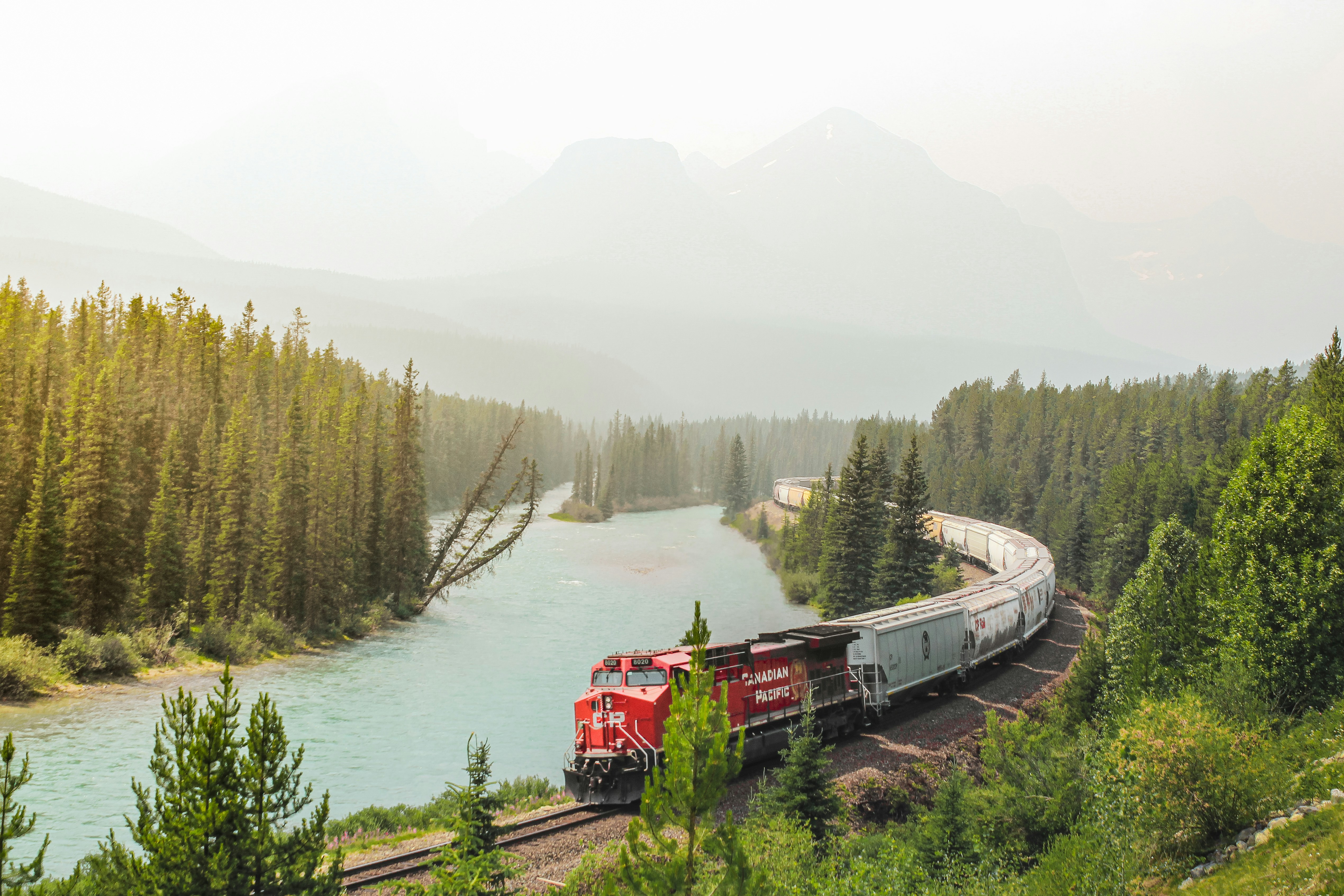 A train traveling down train tracks next to a river photo – Free Banff ...