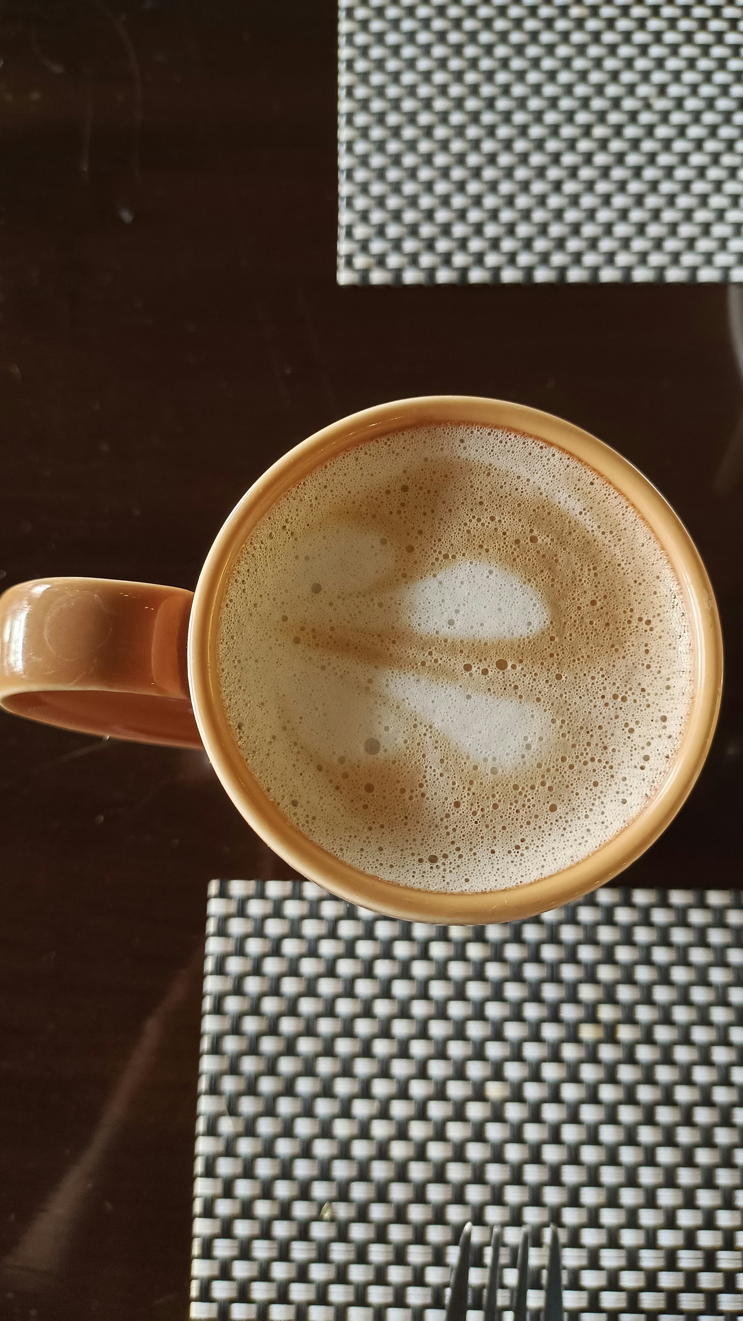 A top-down view of a coffee cup showcasing intricate foam patterns, surrounded by a textured placemat. The warm hues invite a sense of comfort.