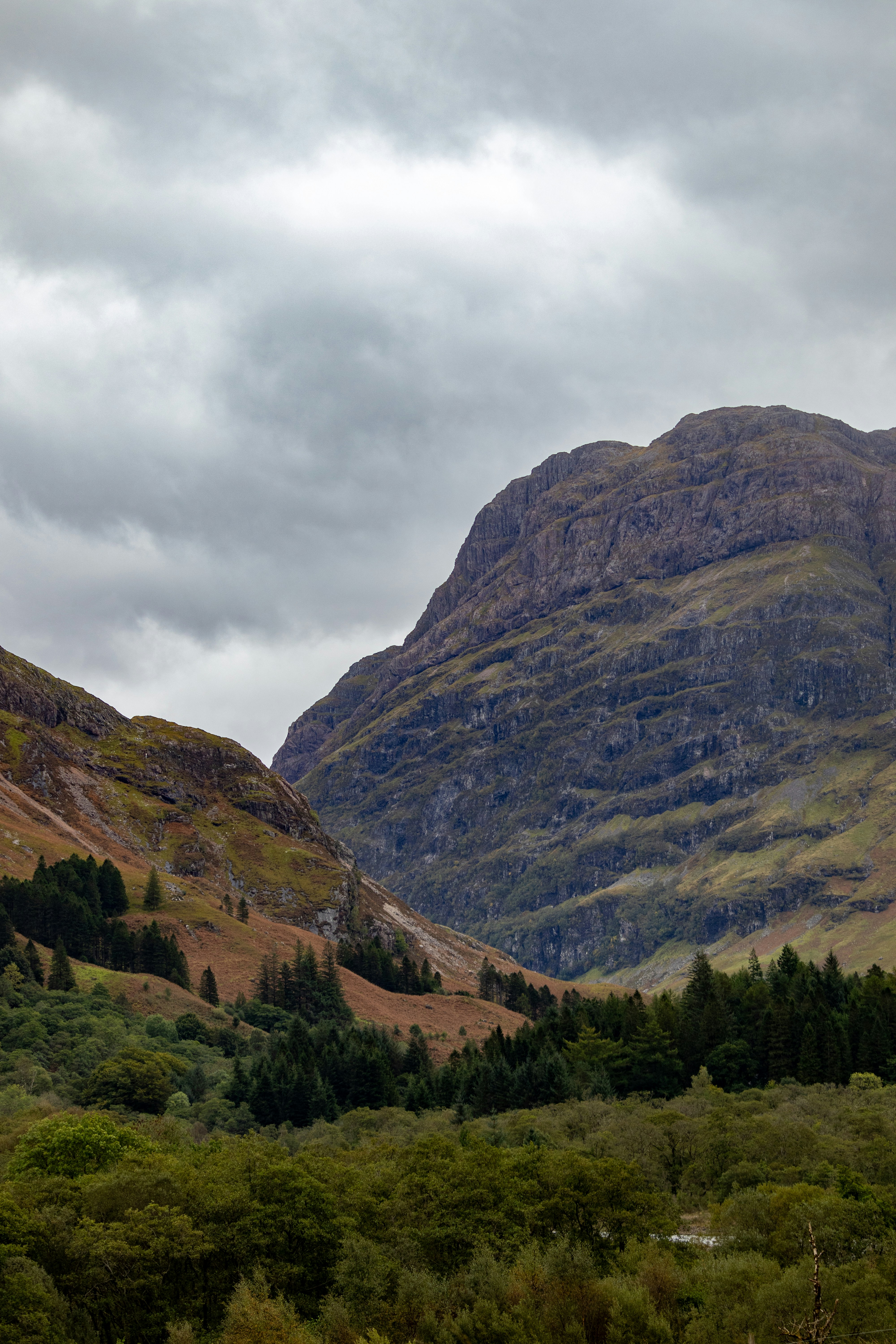 Majestic mountains rise above a lush valley, shrouded in clouds, showcasing the rugged beauty of the landscape.