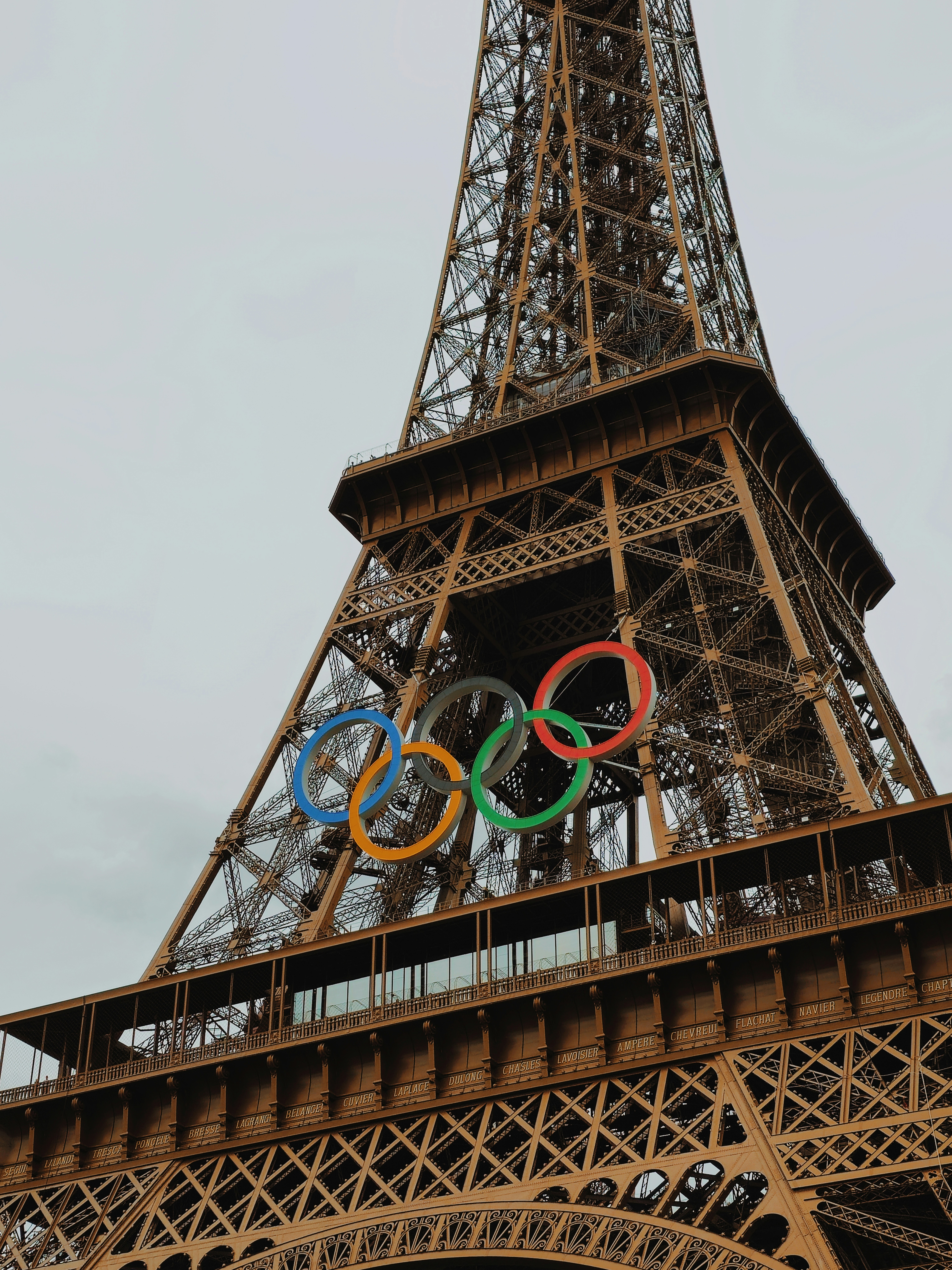 Eiffel Tower adorned with the Olympic rings, symbolizing unity and sportsmanship in a historic city. The cloudy sky adds a dramatic backdrop.