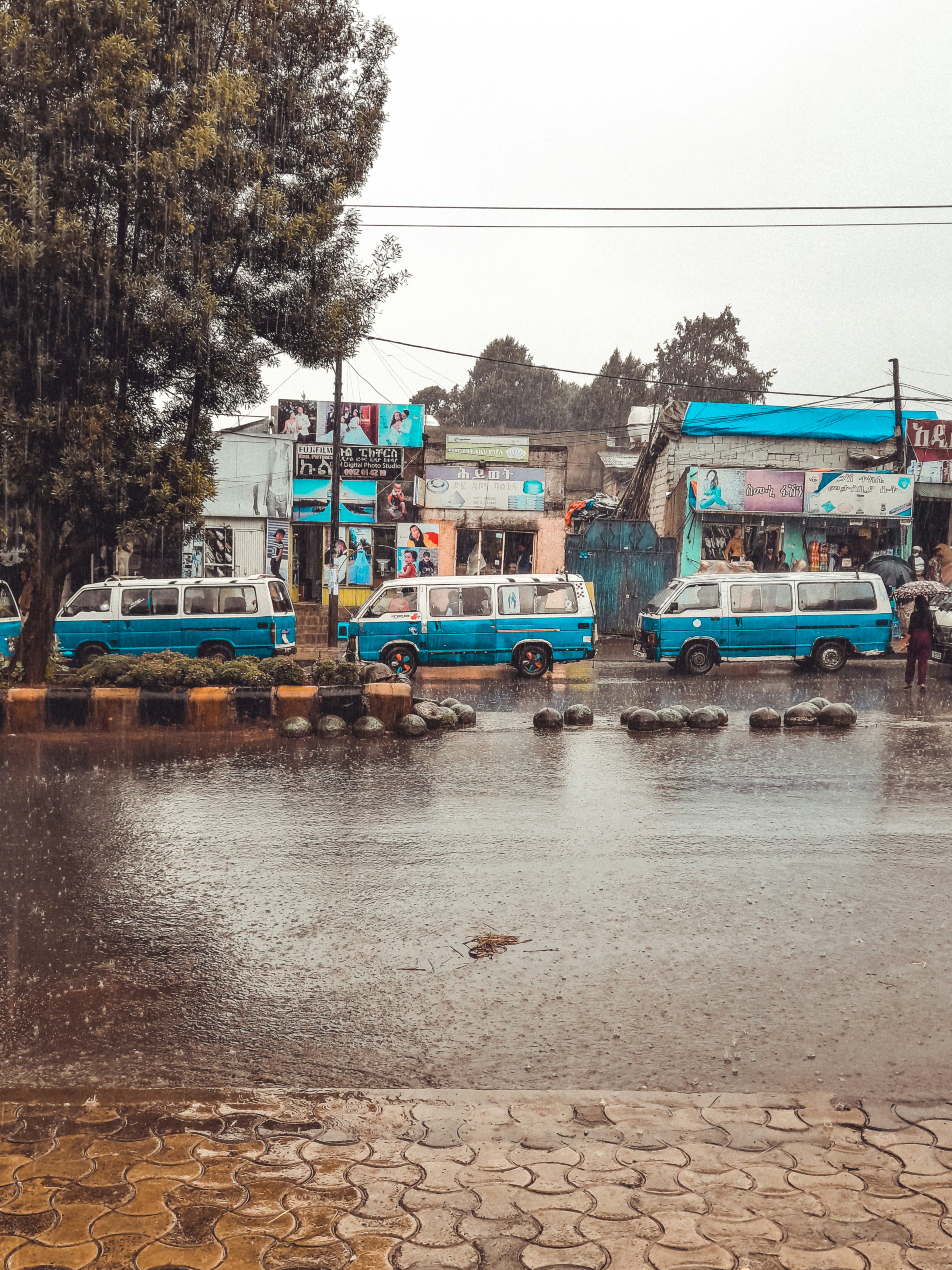Blue minibuses on a rain-soaked street beside a row of shops