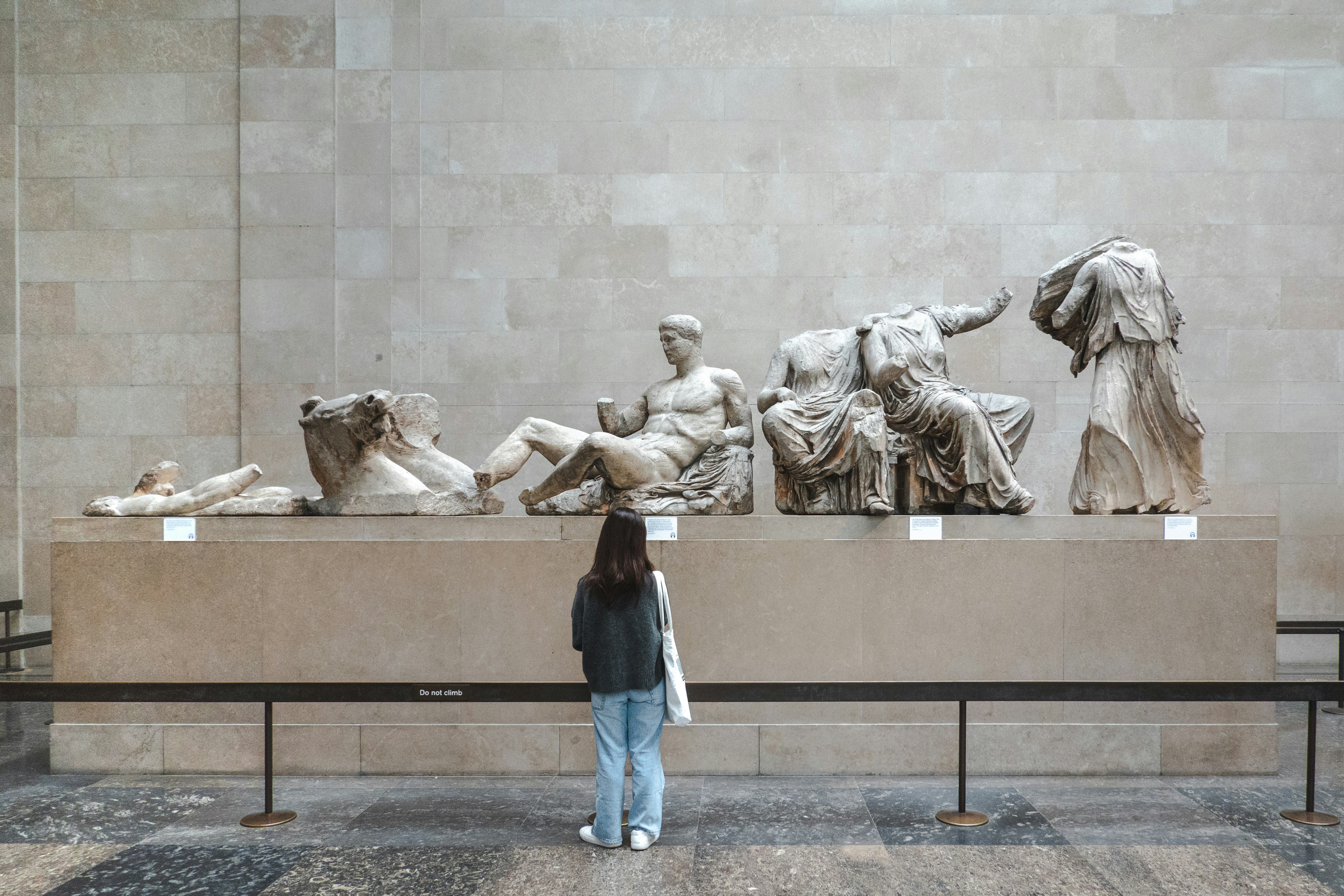 A visitor stands before a collection of ancient sculptures, engaging with the remnants of classical art displayed in a modern museum setting.