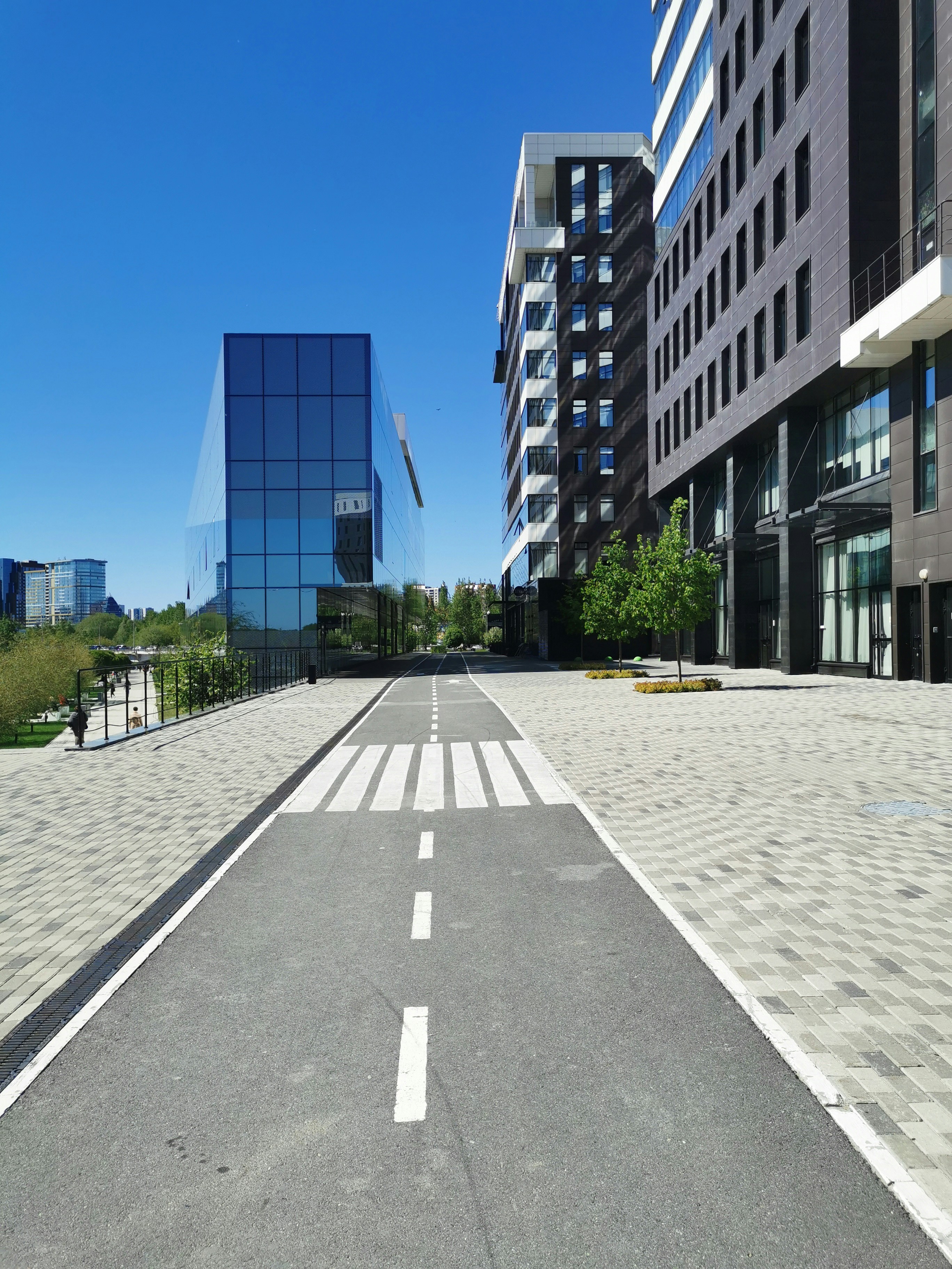 Wide pathway flanked by contemporary buildings, showcasing a blend of glass and stone architecture under a clear blue sky.