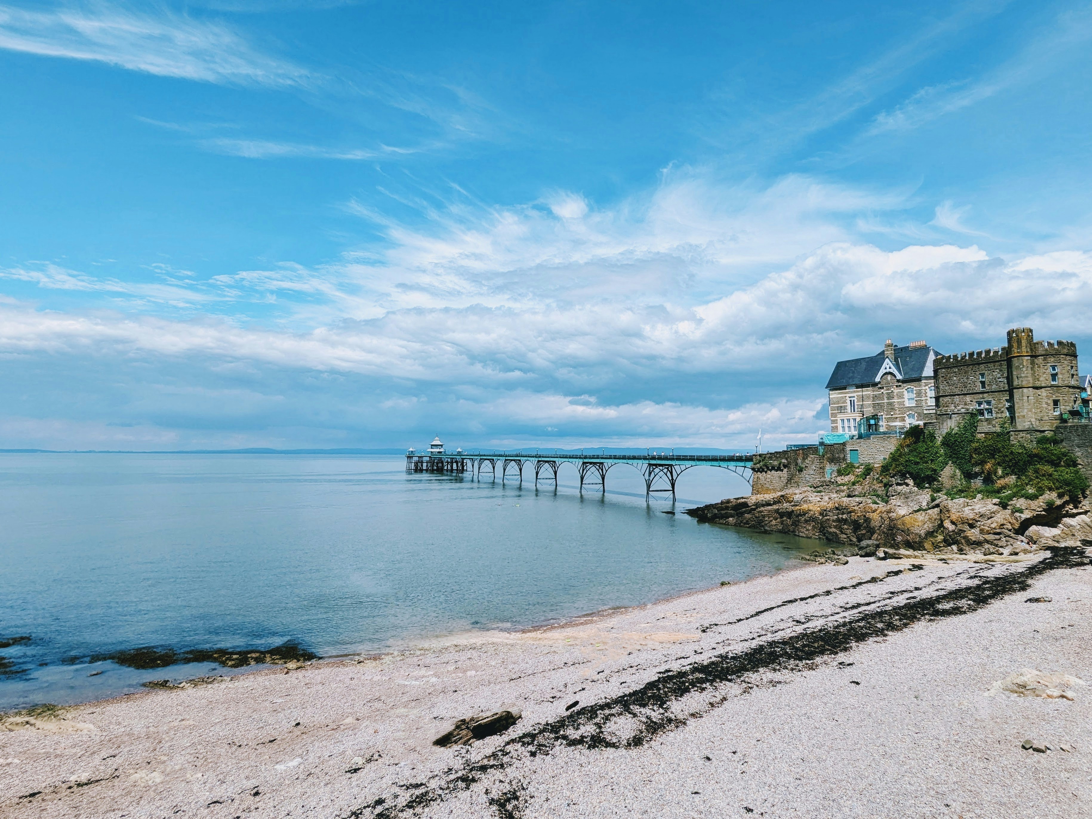 Sandy beach leading to a historic pier under a bright blue sky.