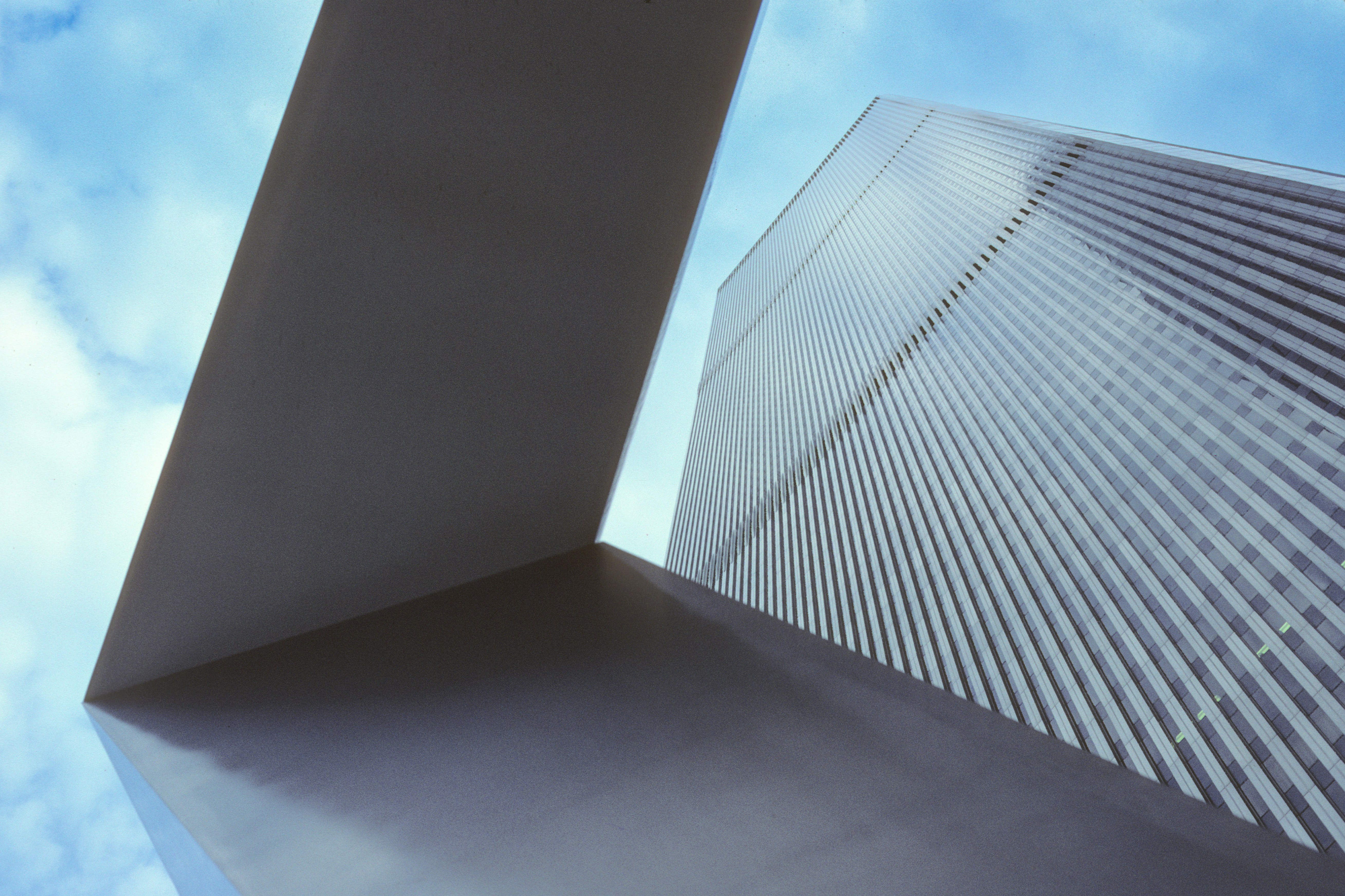 Abstract view of a modern building's facade and overhanging structure against a cloudy sky.