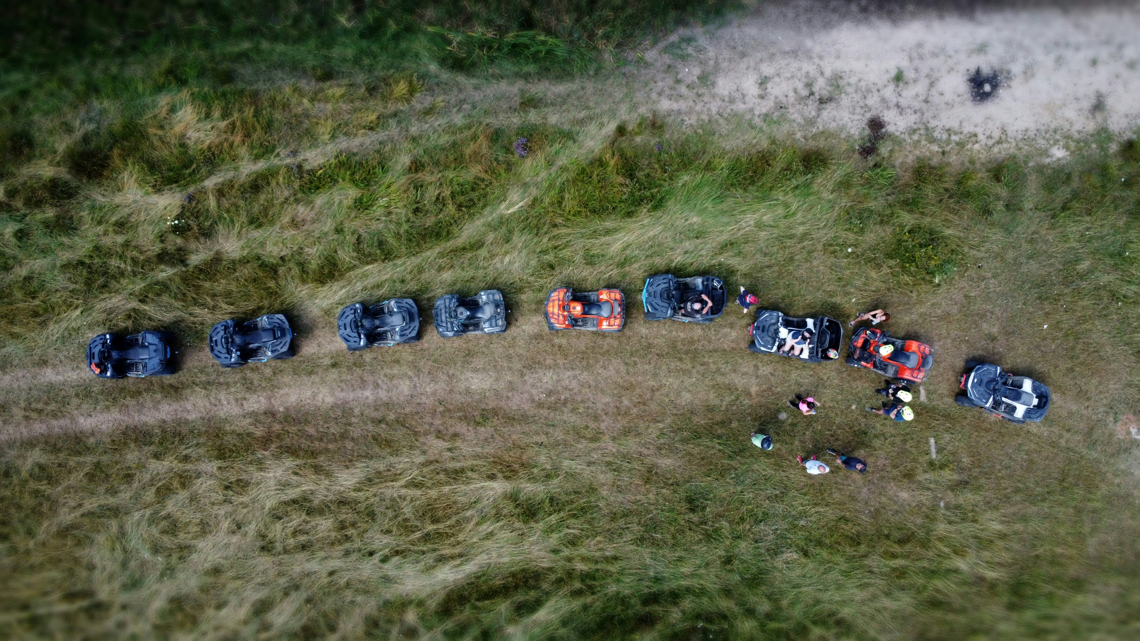 Meadow Convoy: Aerial lineup of rugged rigs and a distant gathering