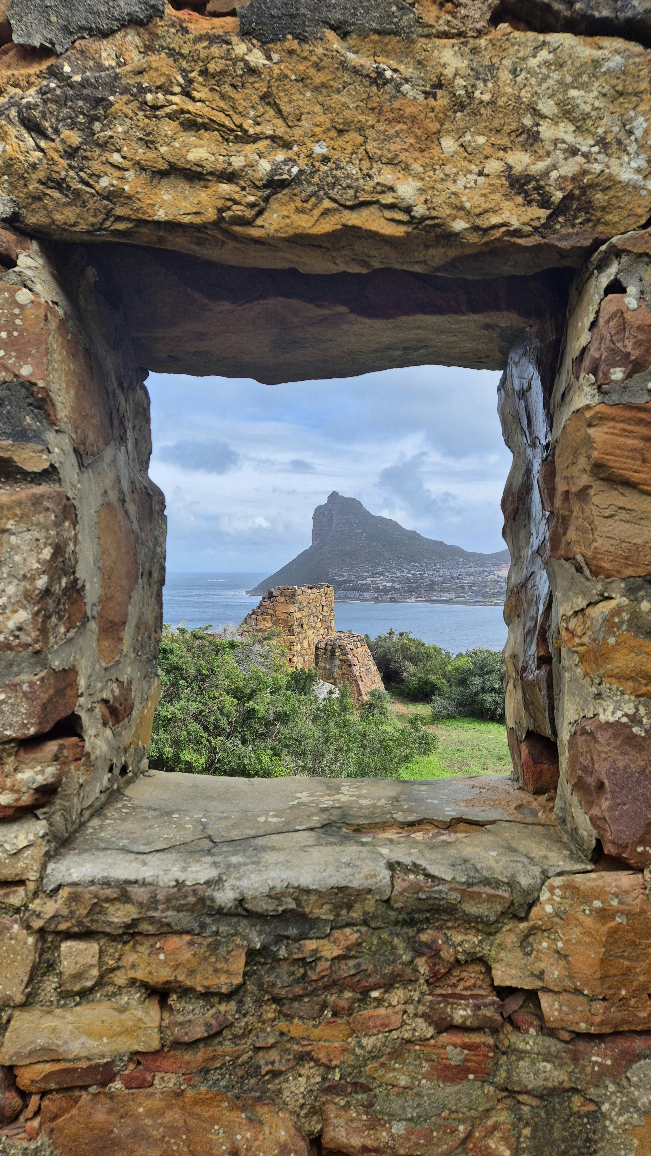Photograph of a weathered brick window framing a distant conical island across a calm sea.