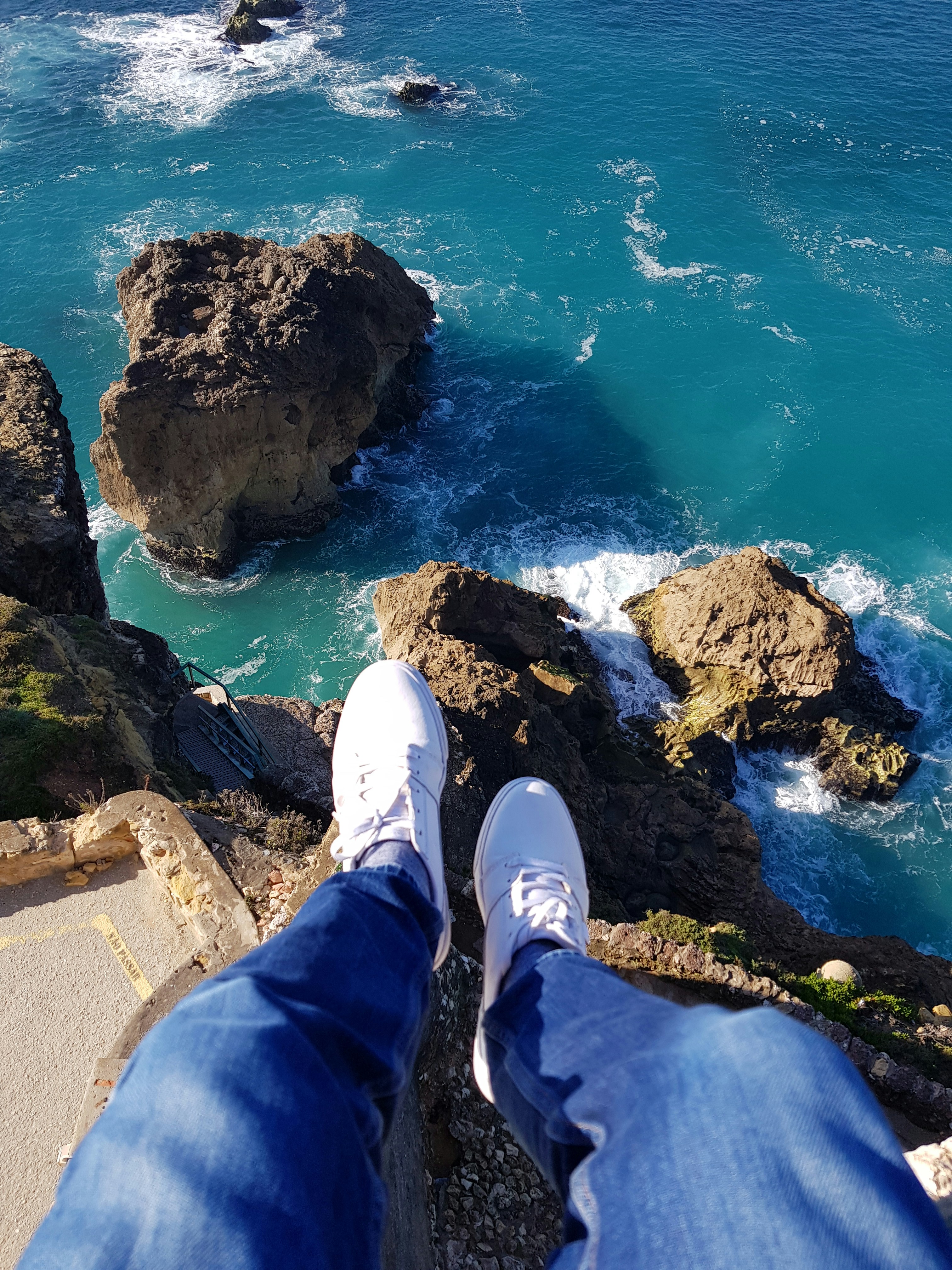 Overhang Above the Atlantic: Shoes Dangle Over Rocky Blue Abyss