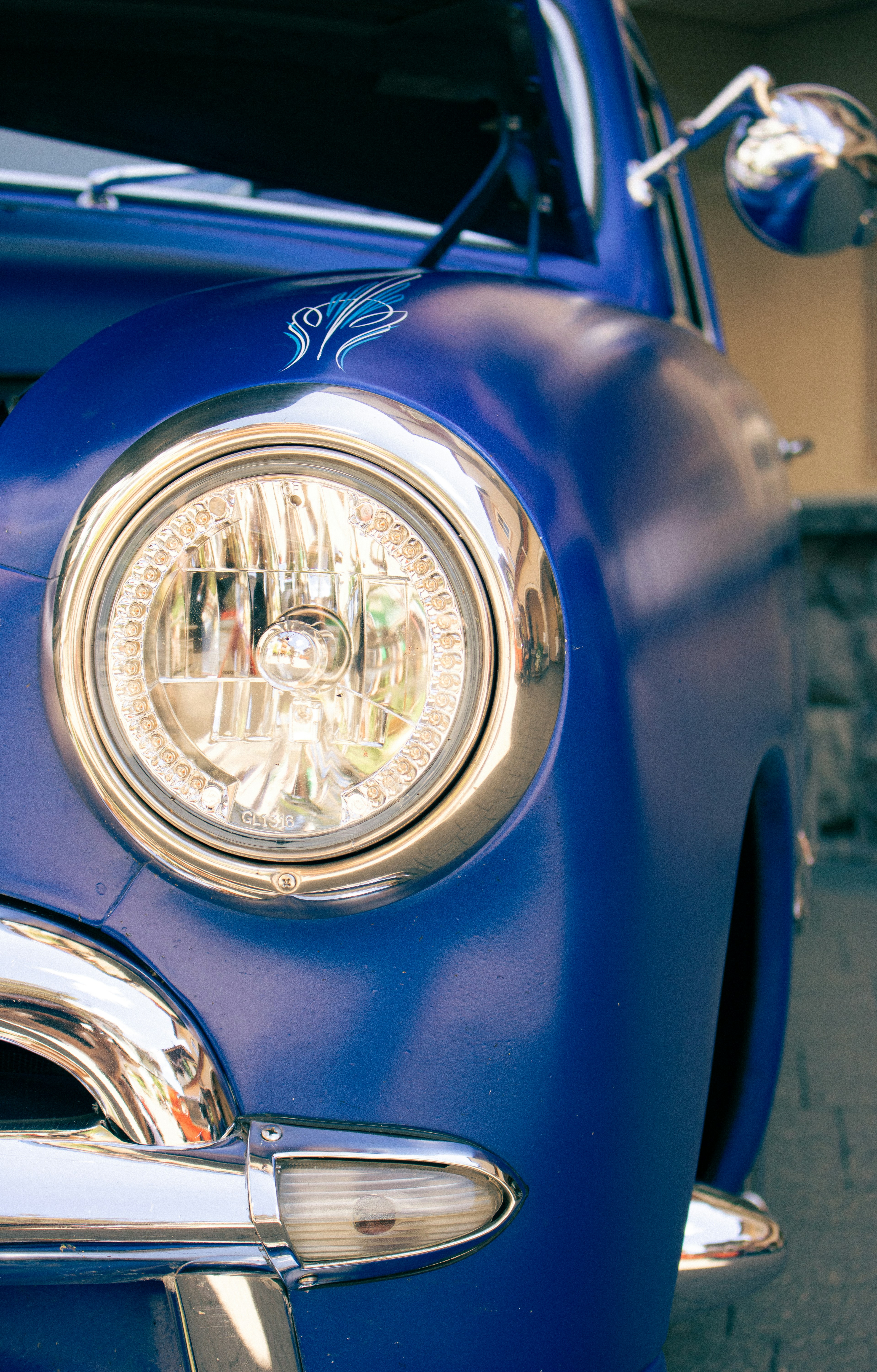 Close-up of a vintage blue car's headlight and chrome detailing, showcasing its unique design elements. The polished surface reflects surrounding colors.