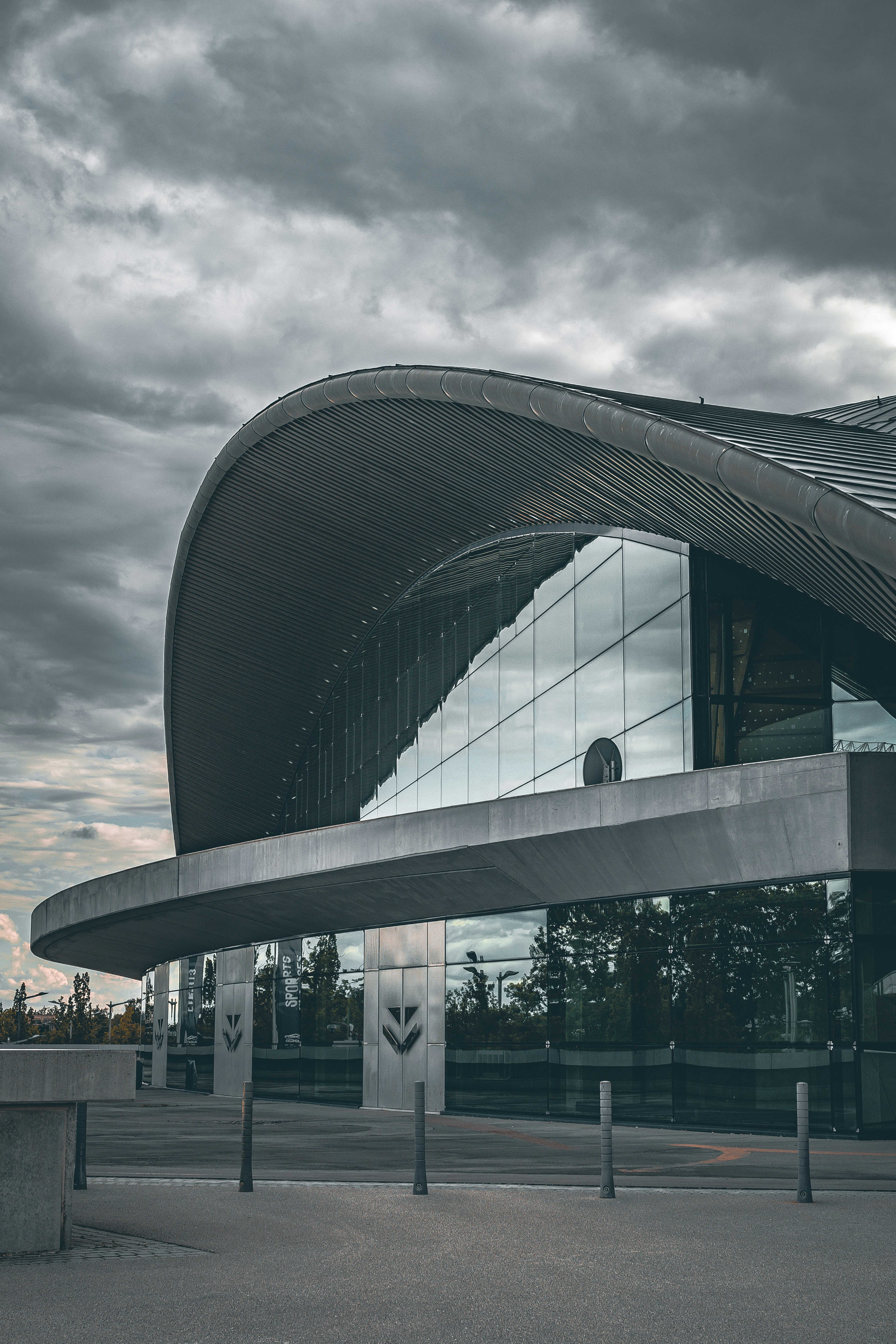 Curved Roof Pavilion Reflects a Cloudy Sky in Glass and Steel