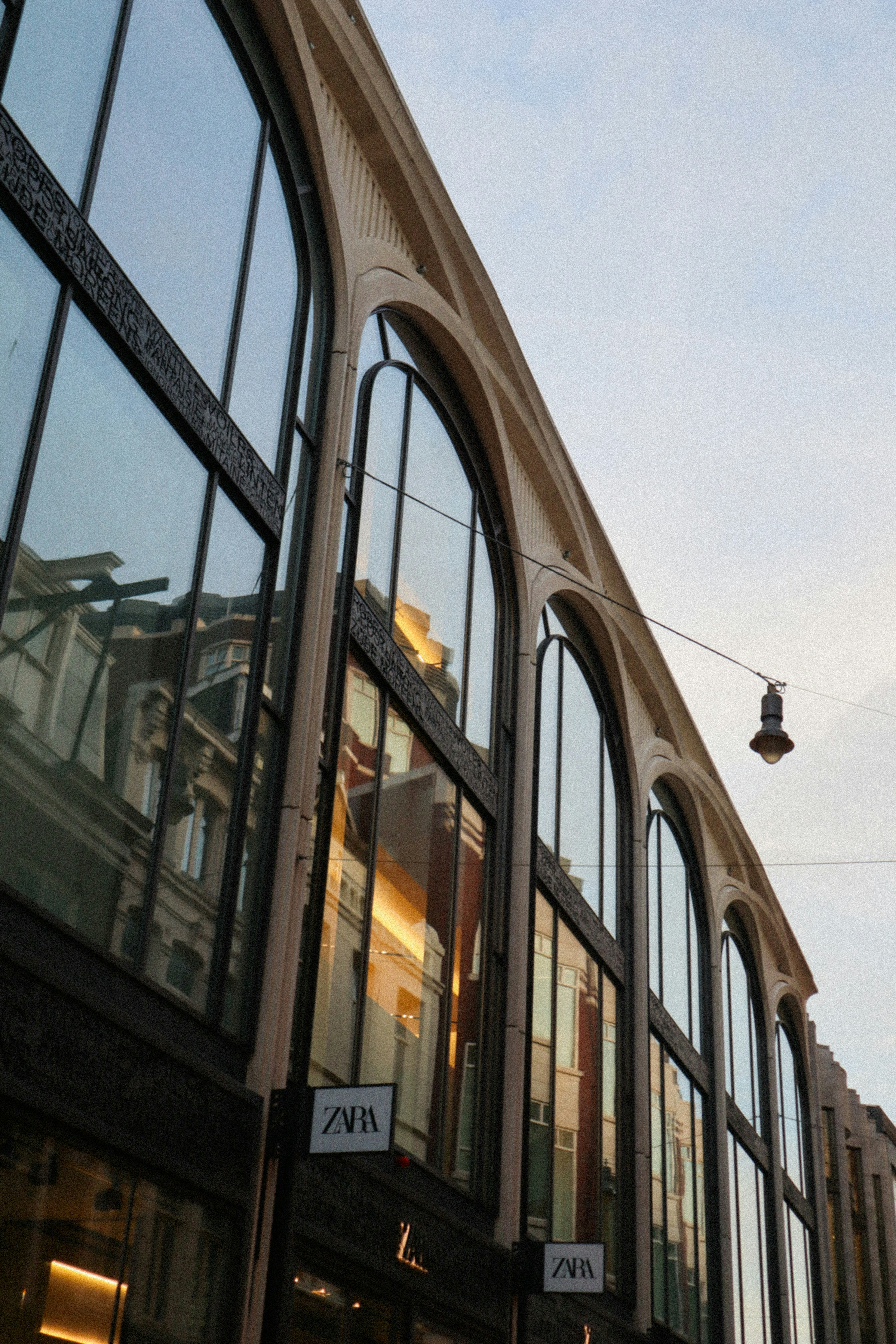 Arched Glass and Zara Facades: Reflections Along a City Arcade