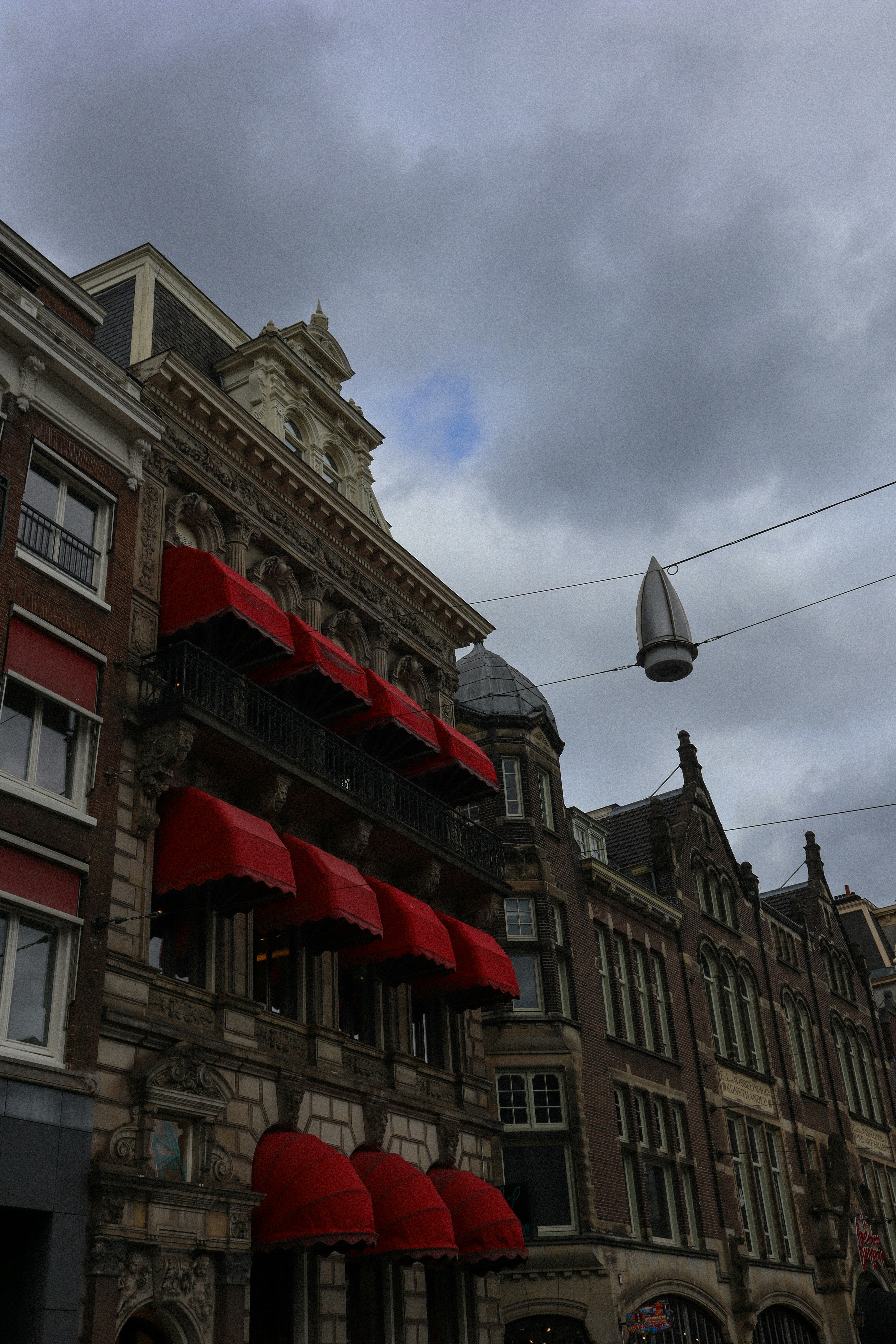 Historic building adorned with vibrant red awnings, contrasting against a cloudy sky. Architectural details highlight the charm of the urban landscape.