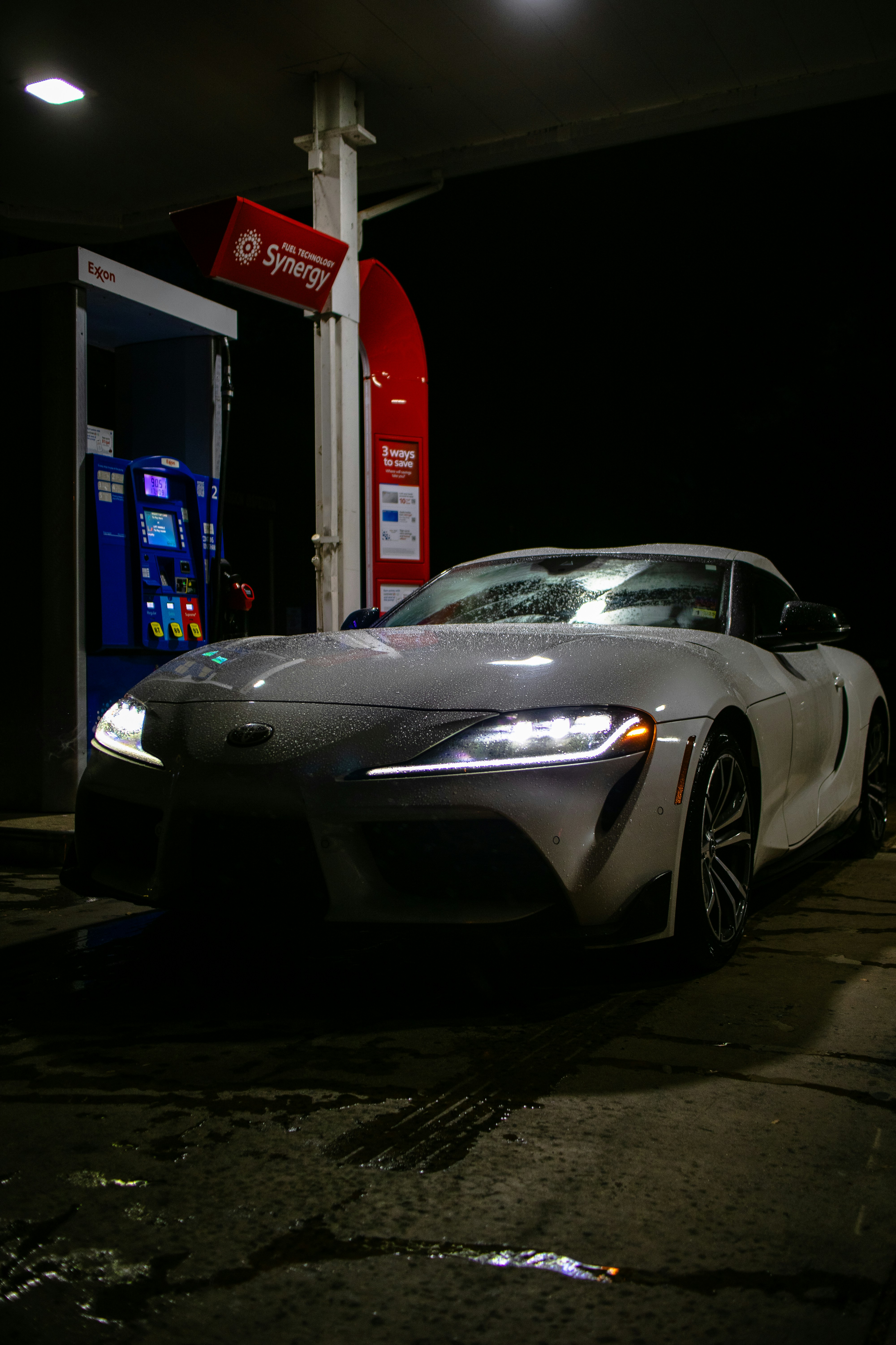 Neon Reflections on a Silver Sports Car at a Quiet Night Gas Station