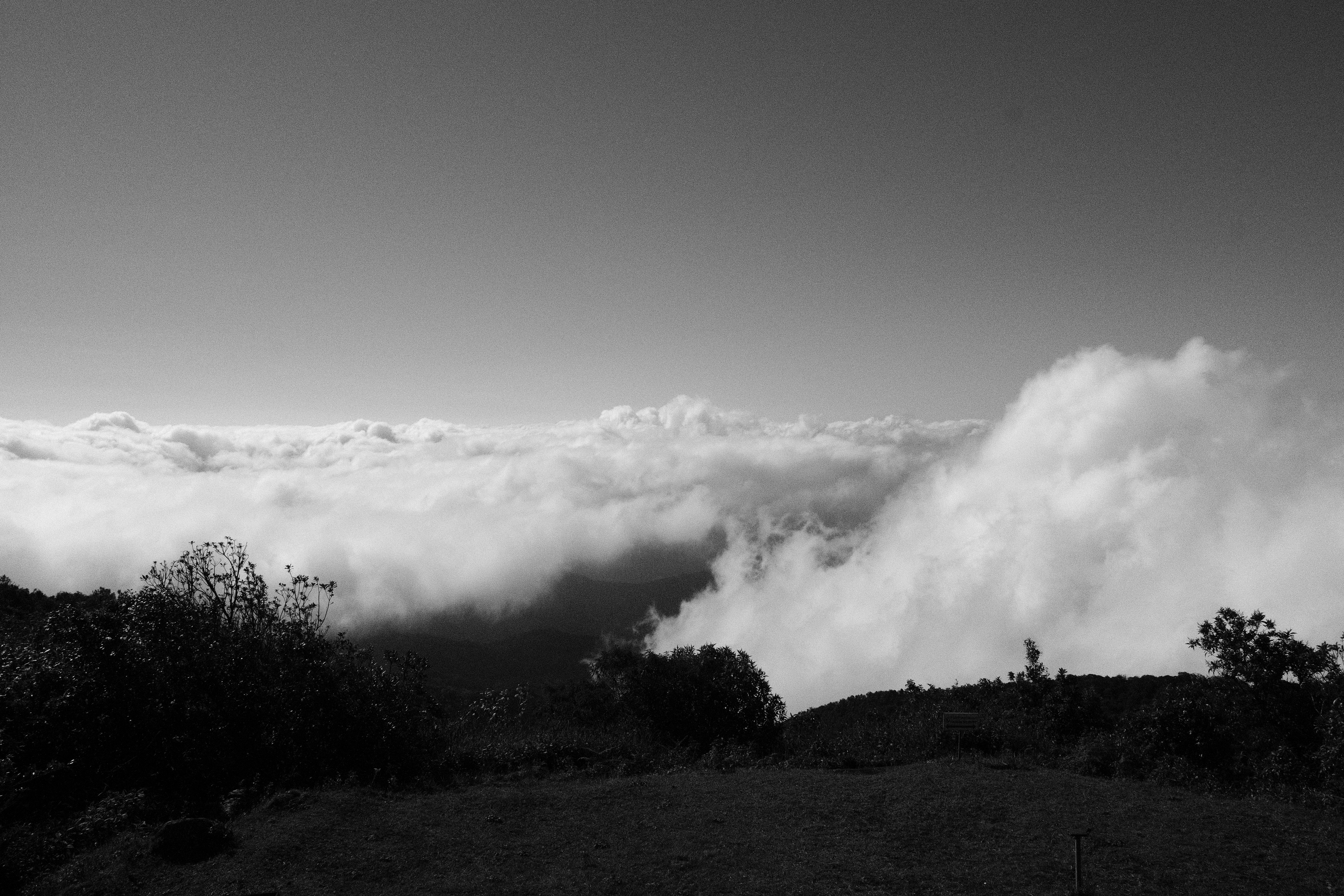 Black and white landscape of clouds rolling over a hillside under a clear sky.