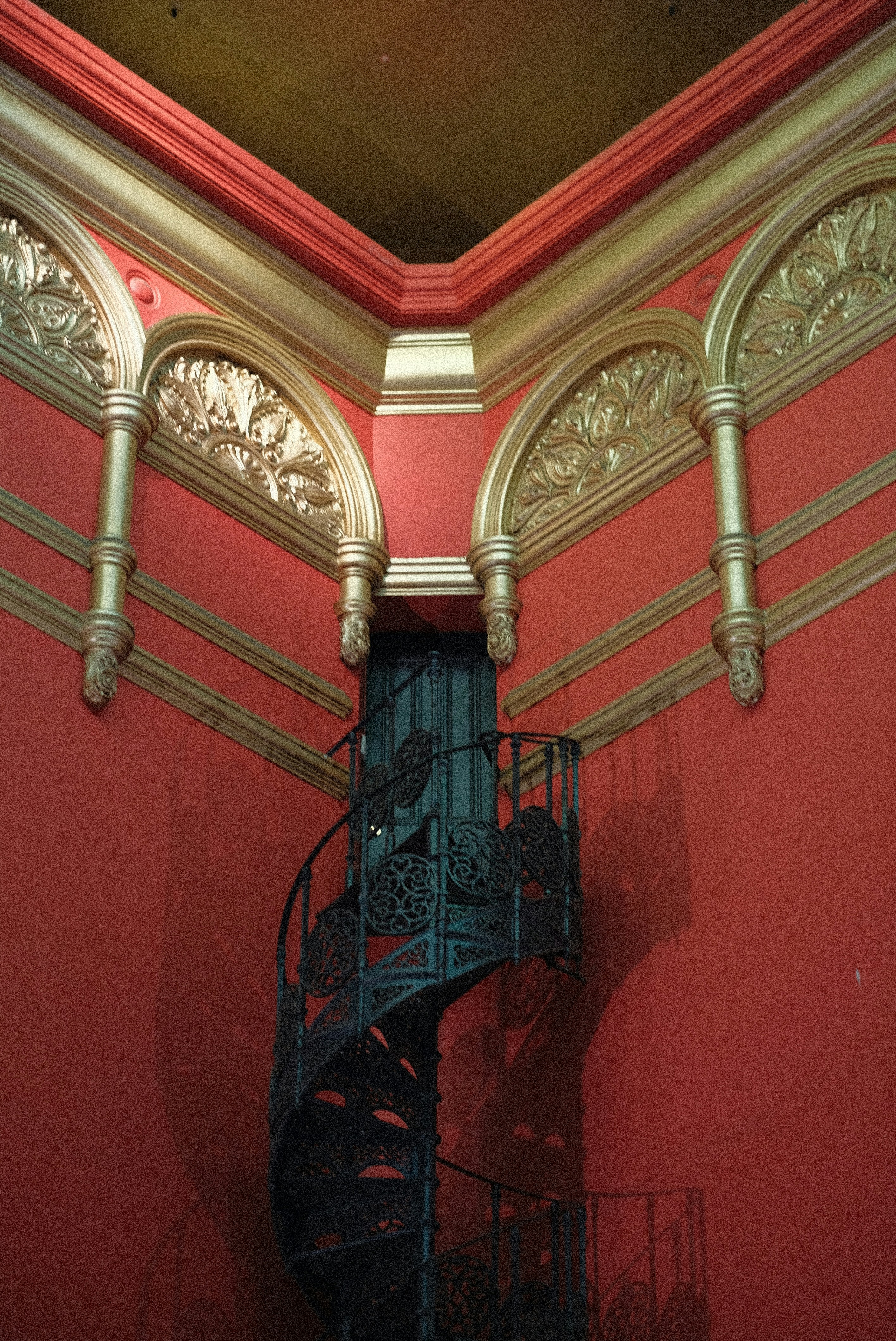 Spiral Iron Staircase under gilded arches in a crimson gallery