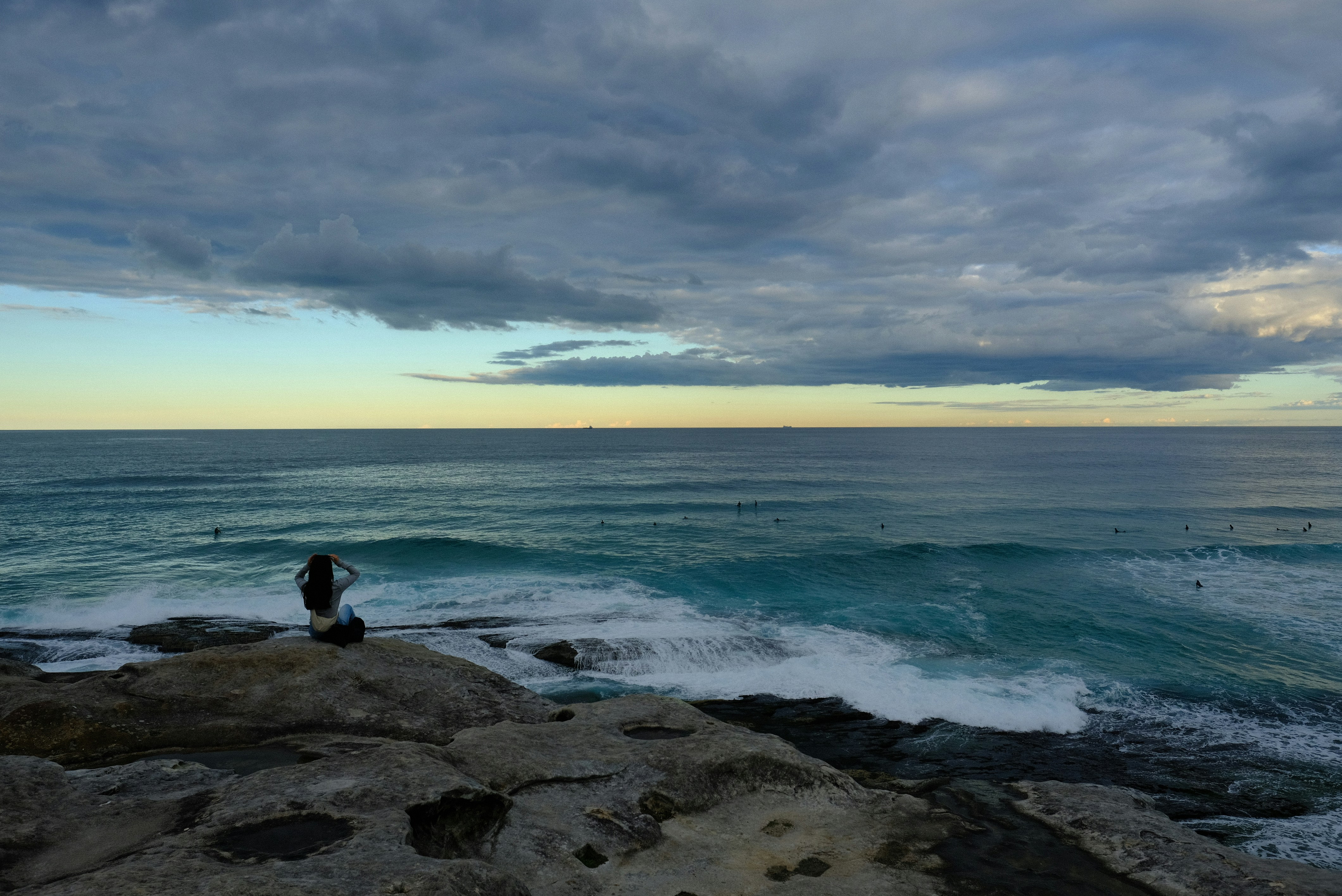 Una persona sentada en una roca mirando hacia el océano foto – Imagen ...