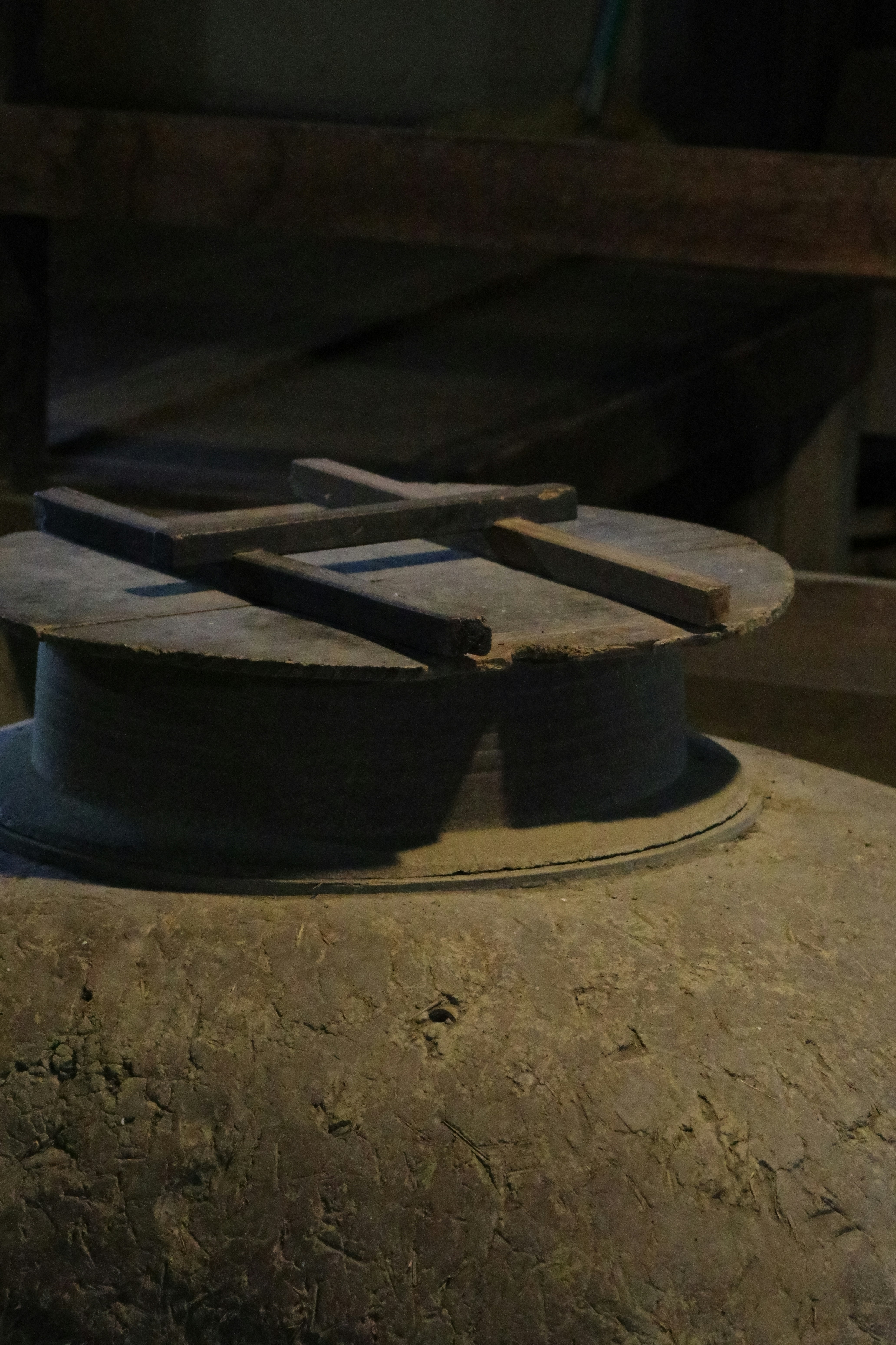 Close-up of a dusty, weathered metal hatch with a cross-shaped handle in a dark, industrial setting.