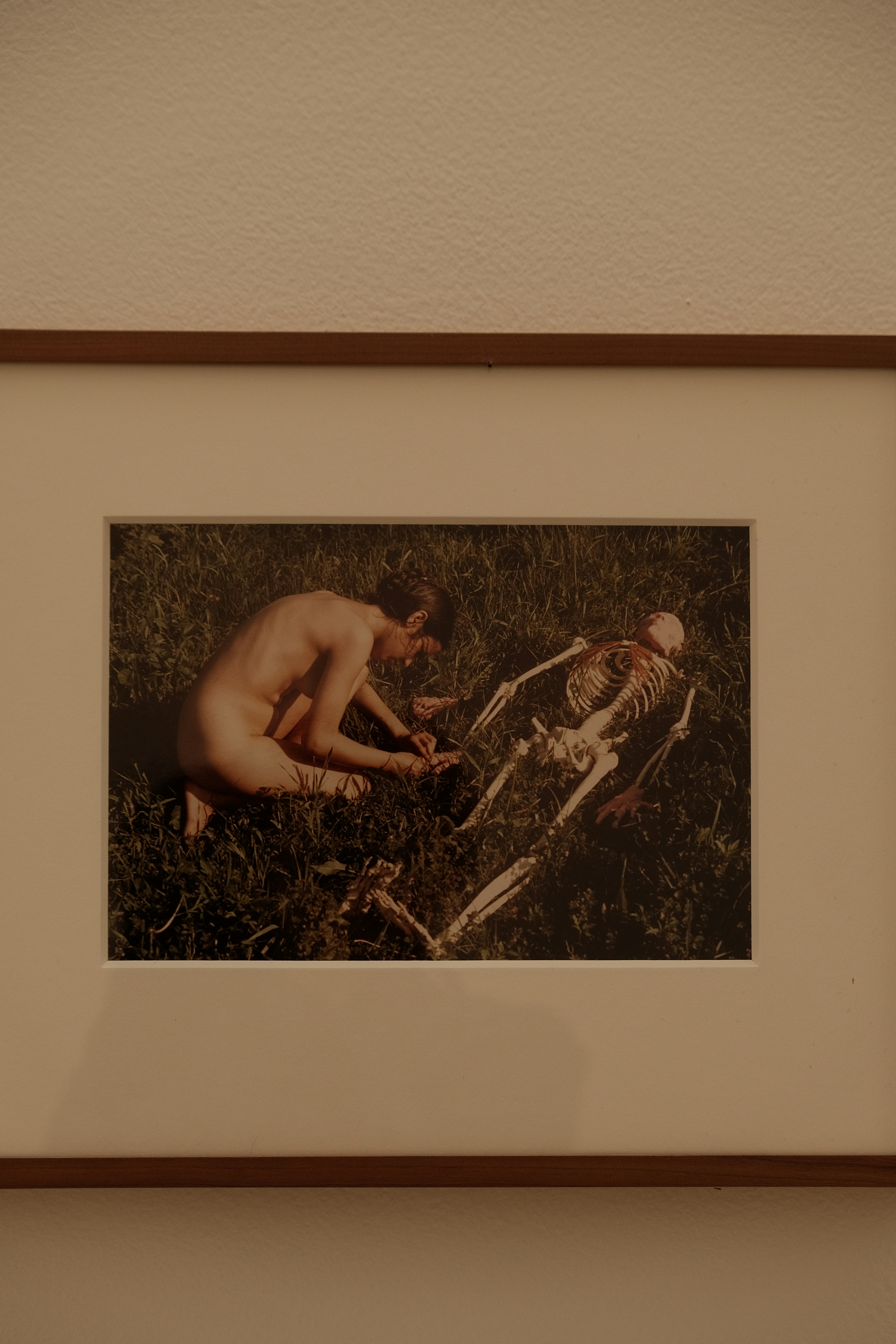 Nude figure tending to a skeletal scene framed in a nostalgic photo