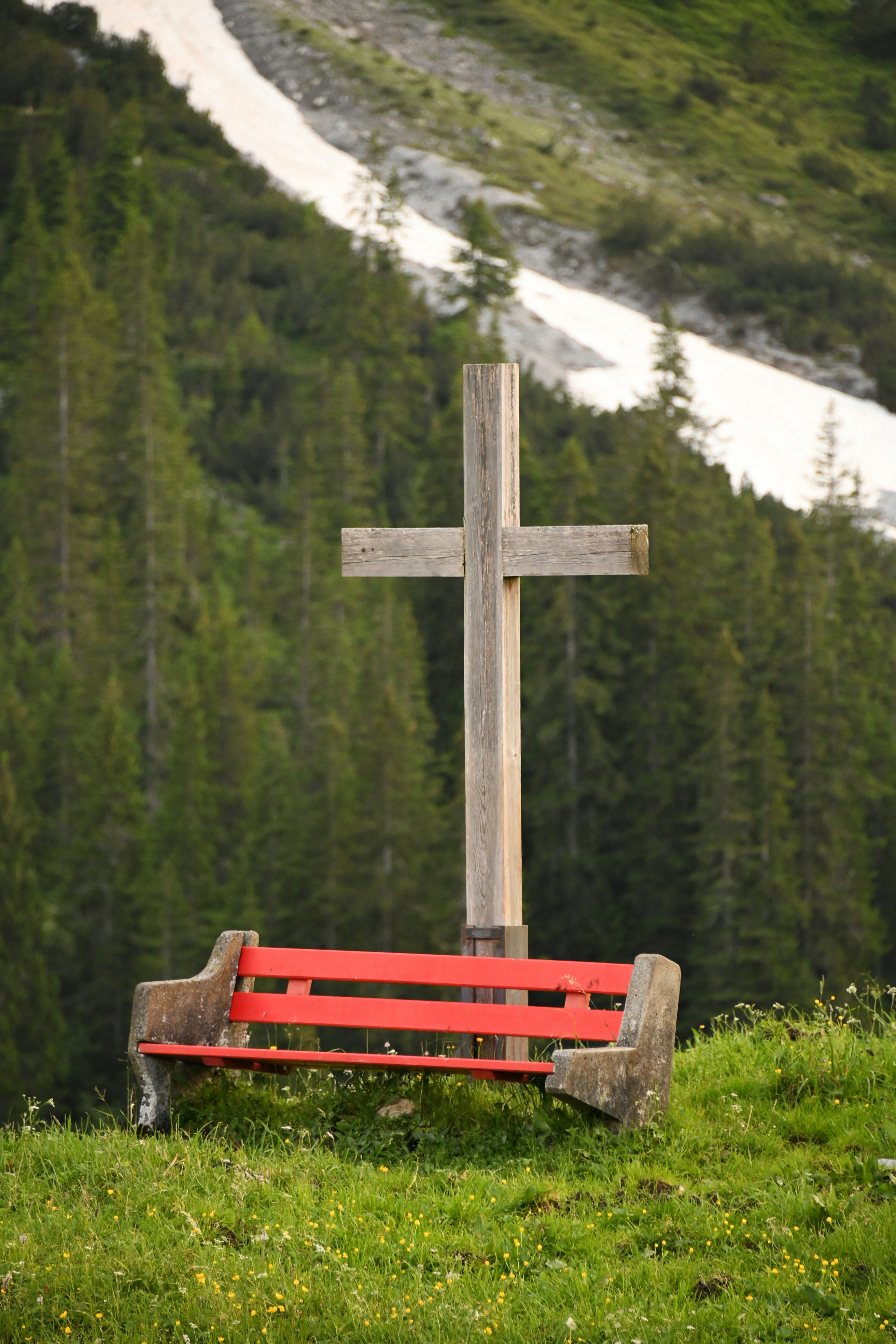Heritage of Silence: Weathered Cross Framed by a Red Bench in Alpine Light