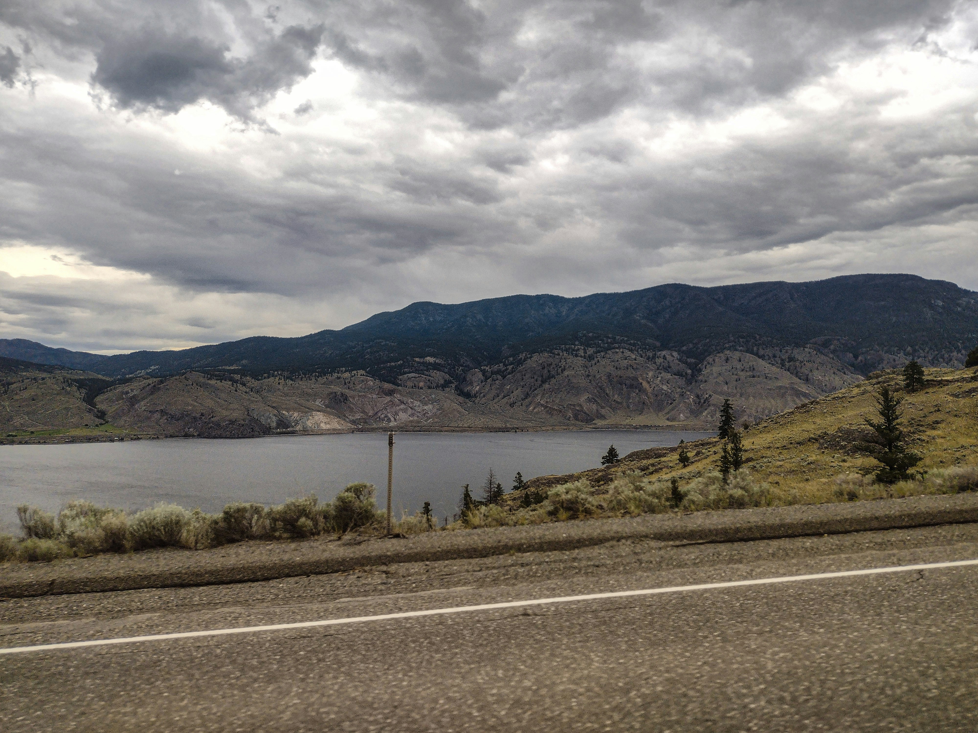 A view of a lake and mountains from the side of a road photo – Free ...