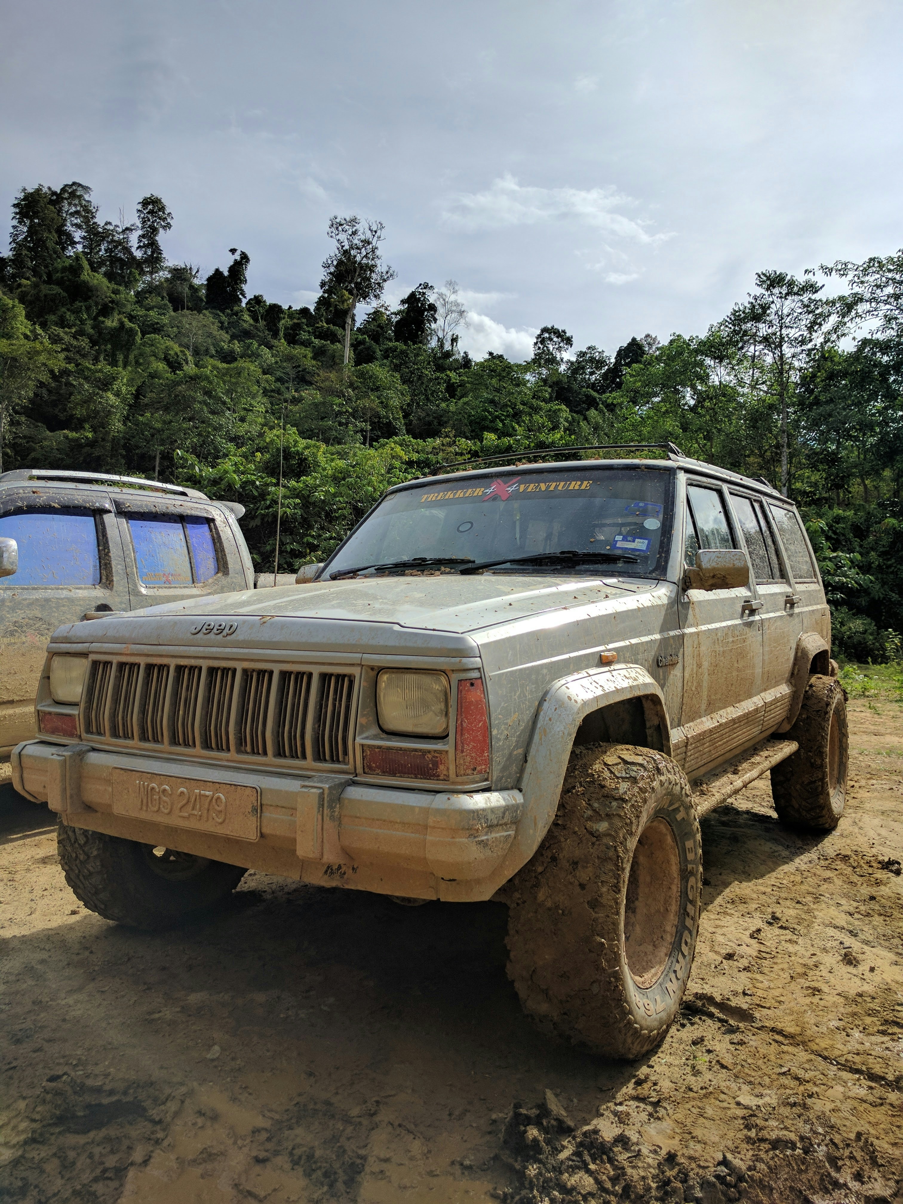 Mud-streaked off-road SUV photographed on a dirt path, with dense green jungle behind.