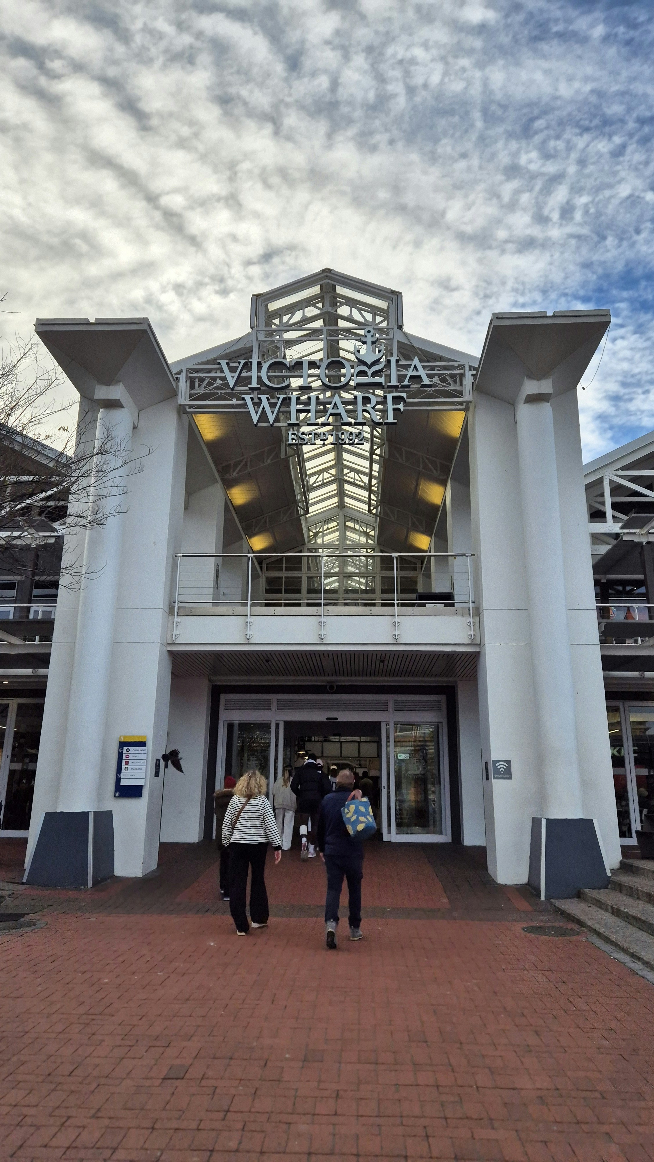 Entrance to Victoria Wharf: People Ascend Under a Glass Roof Toward the Sign