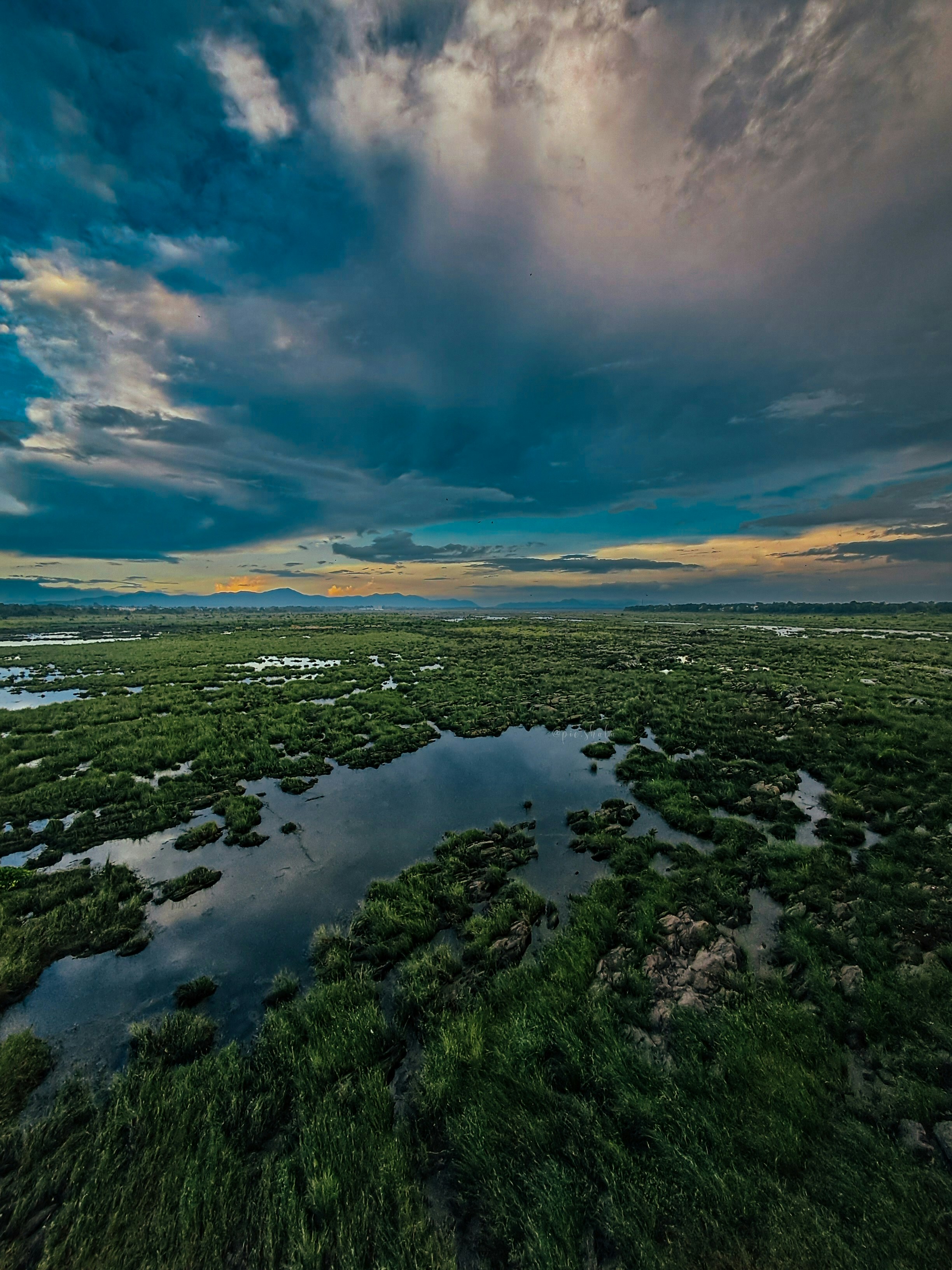 Expansive wetlands under a dramatic sky with varied cloud formations and lush greenery.